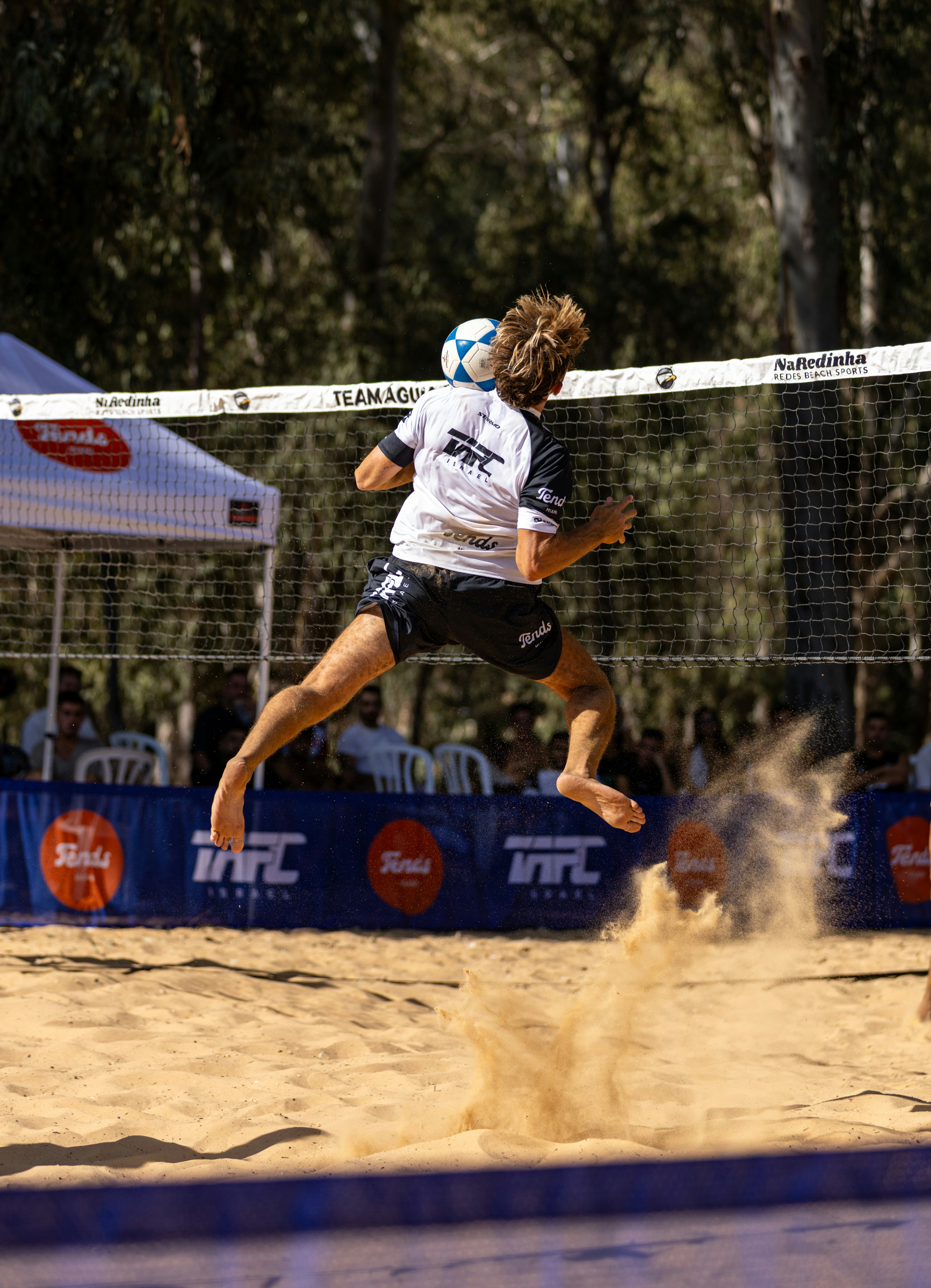 Midair spike over a sunlit sand court during a beach volleyball match