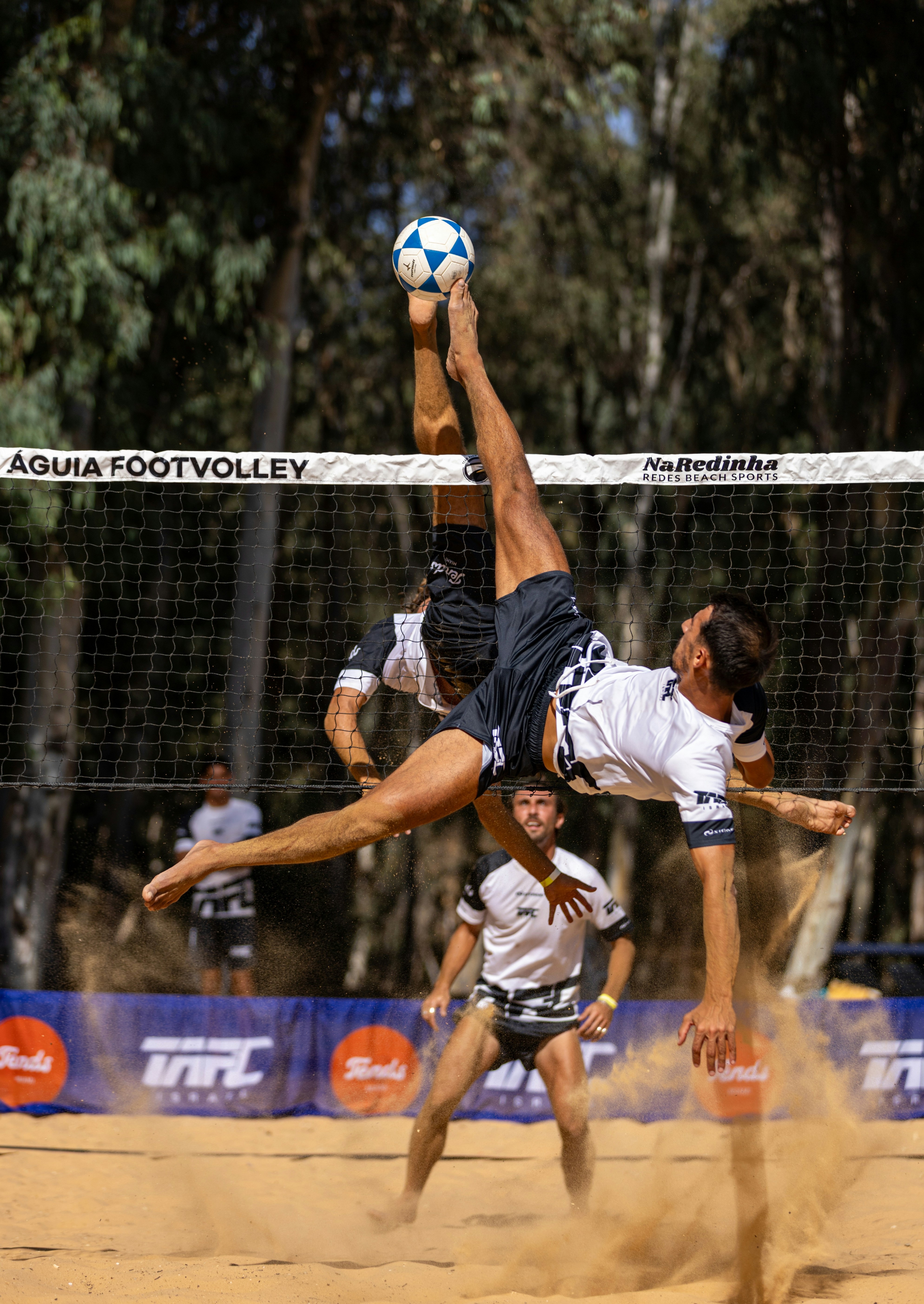 Man performs acrobatic kick during beach footvolley match