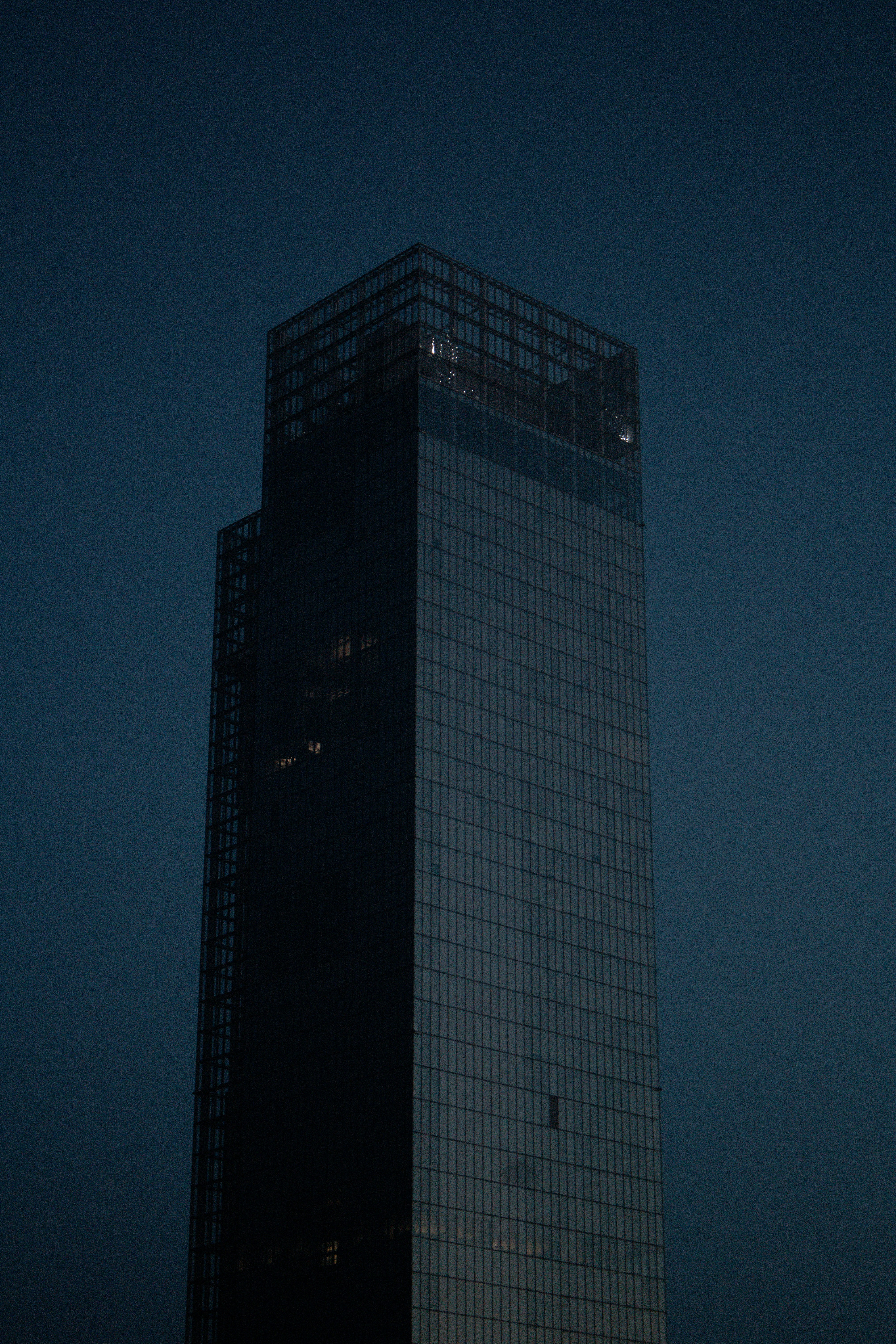 A modern skyscraper silhouetted against the twilight sky, showcasing a blend of glass and steel architecture. Illuminated windows hint at life within.