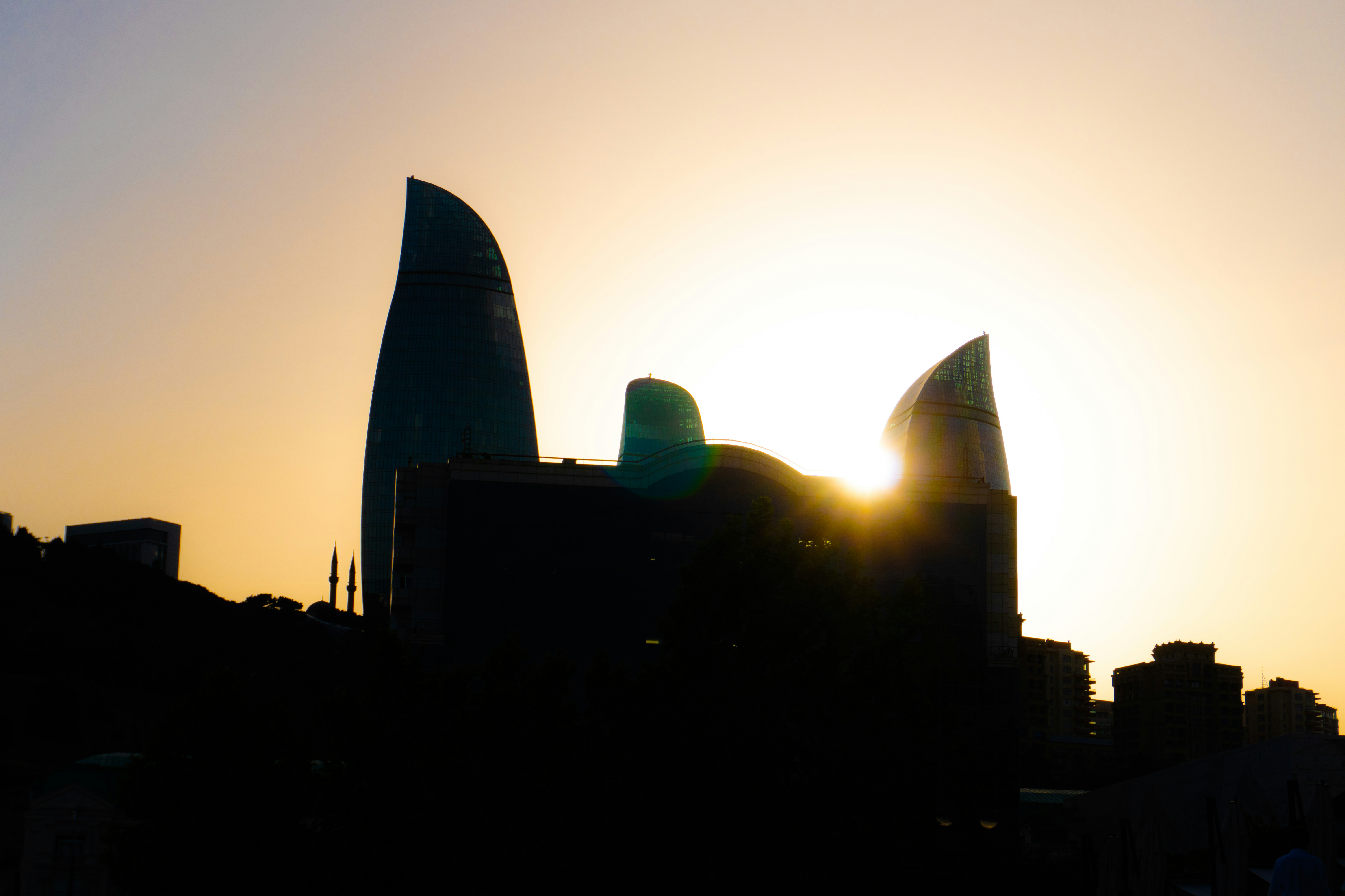 Silhouettes of modern skyscrapers against a glowing sunset, highlighting architectural forms and urban landscape.