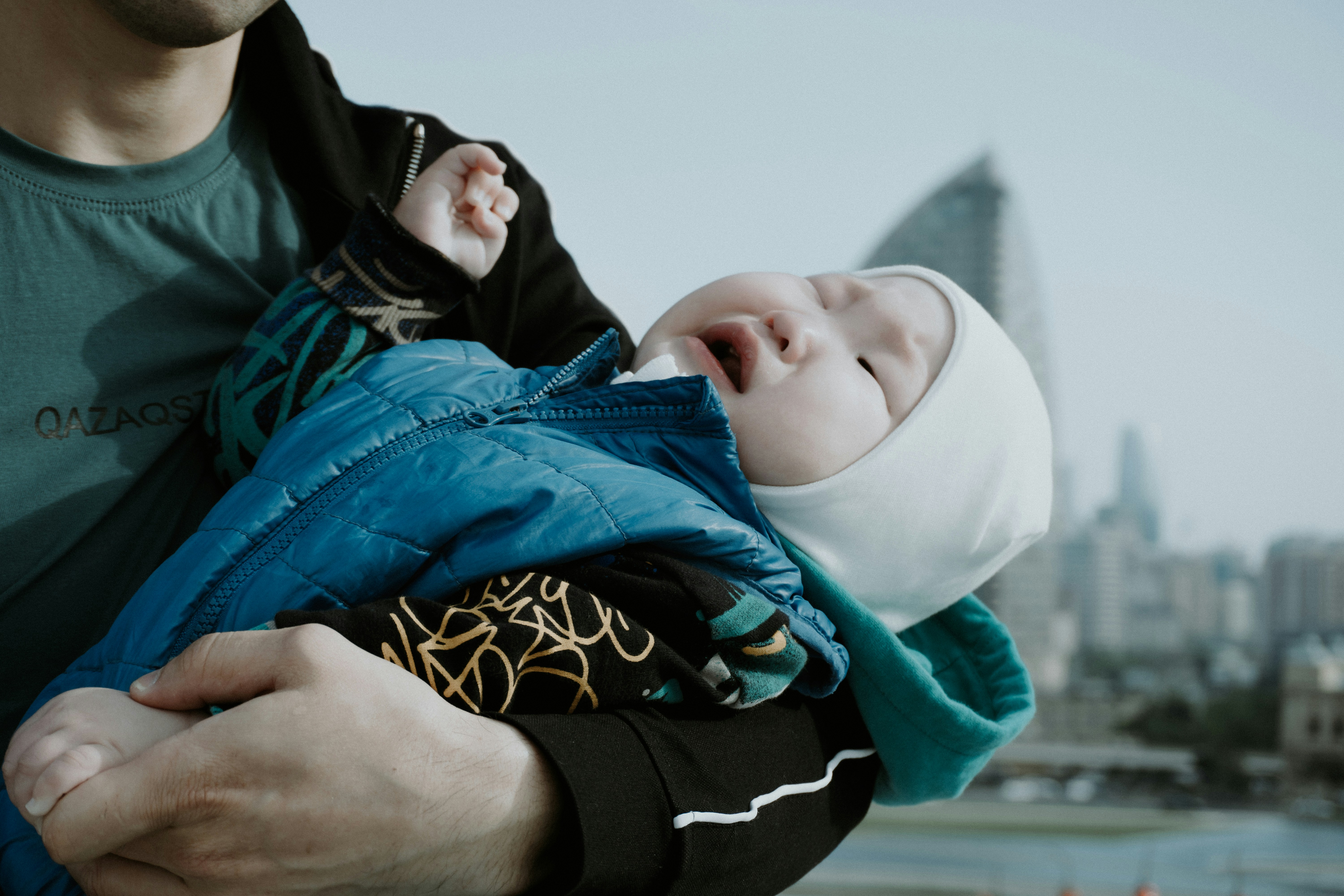 Yawning in the City: A Baby Embraced Against a Modern Skyline