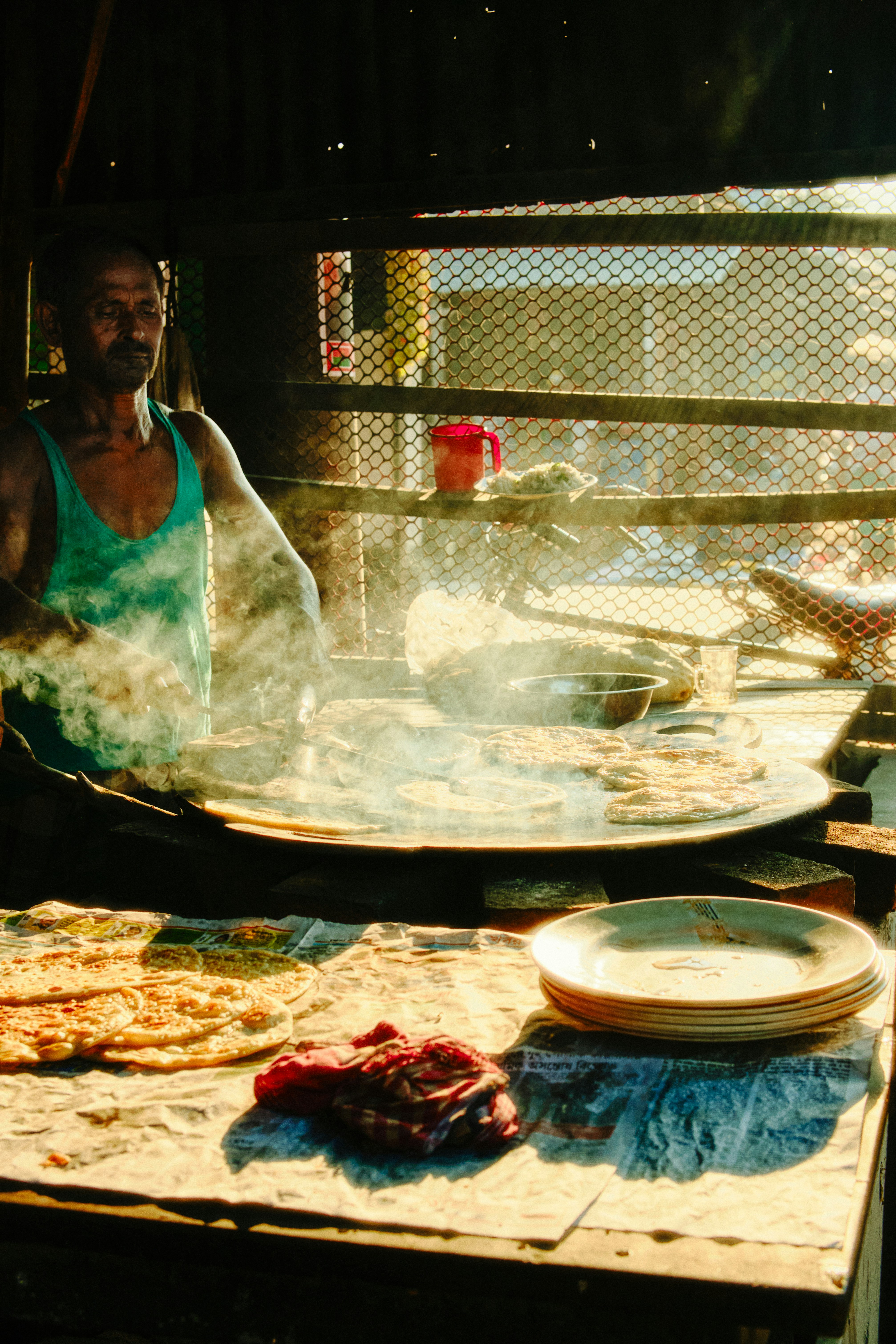 A street vendor skillfully prepares food amidst swirling steam and warm sunlight, showcasing vibrant dishes on a rustic table.