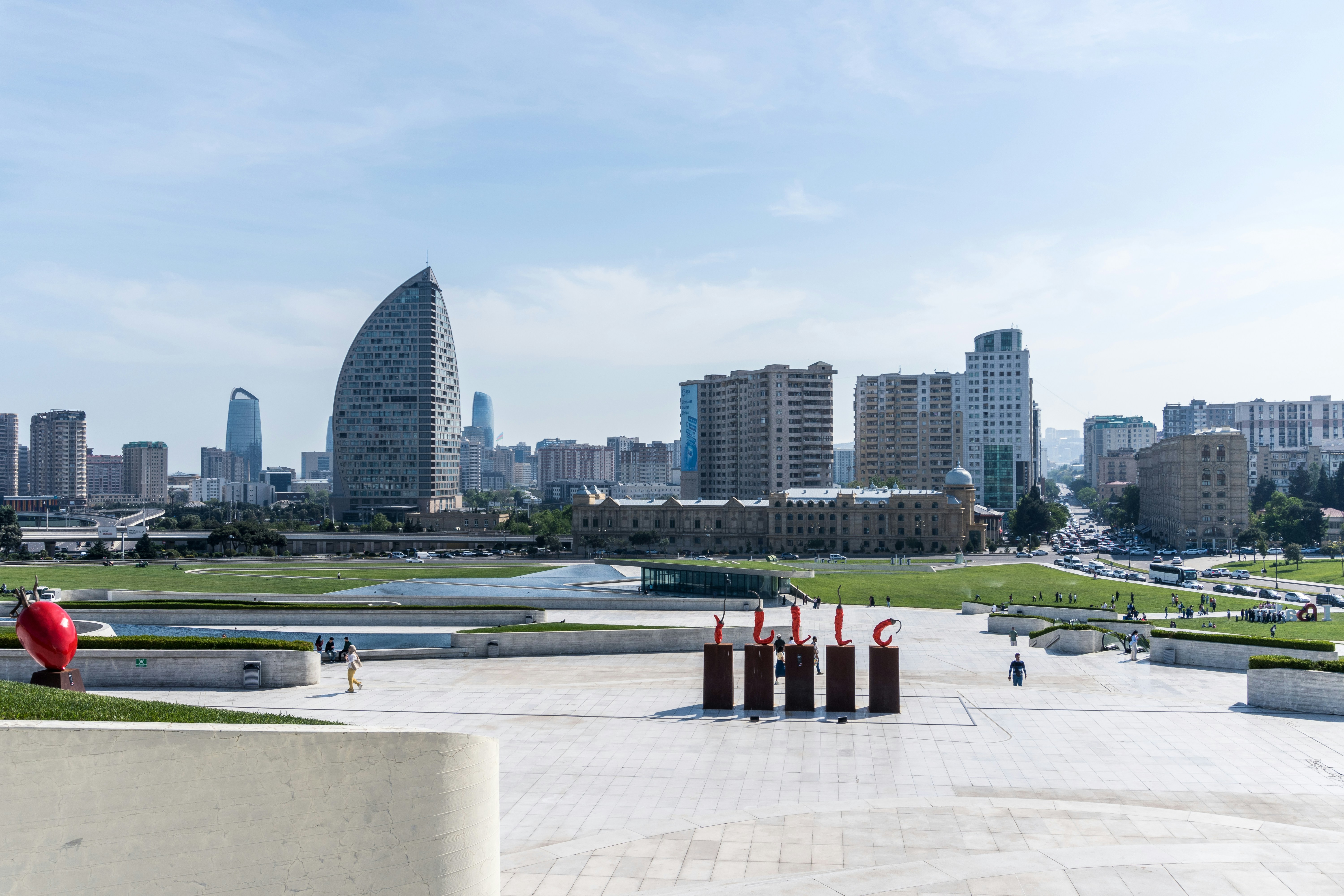 Red Sculptural Row at a Sunlit Riverside Plaza Beneath a Sail-Like Skyline