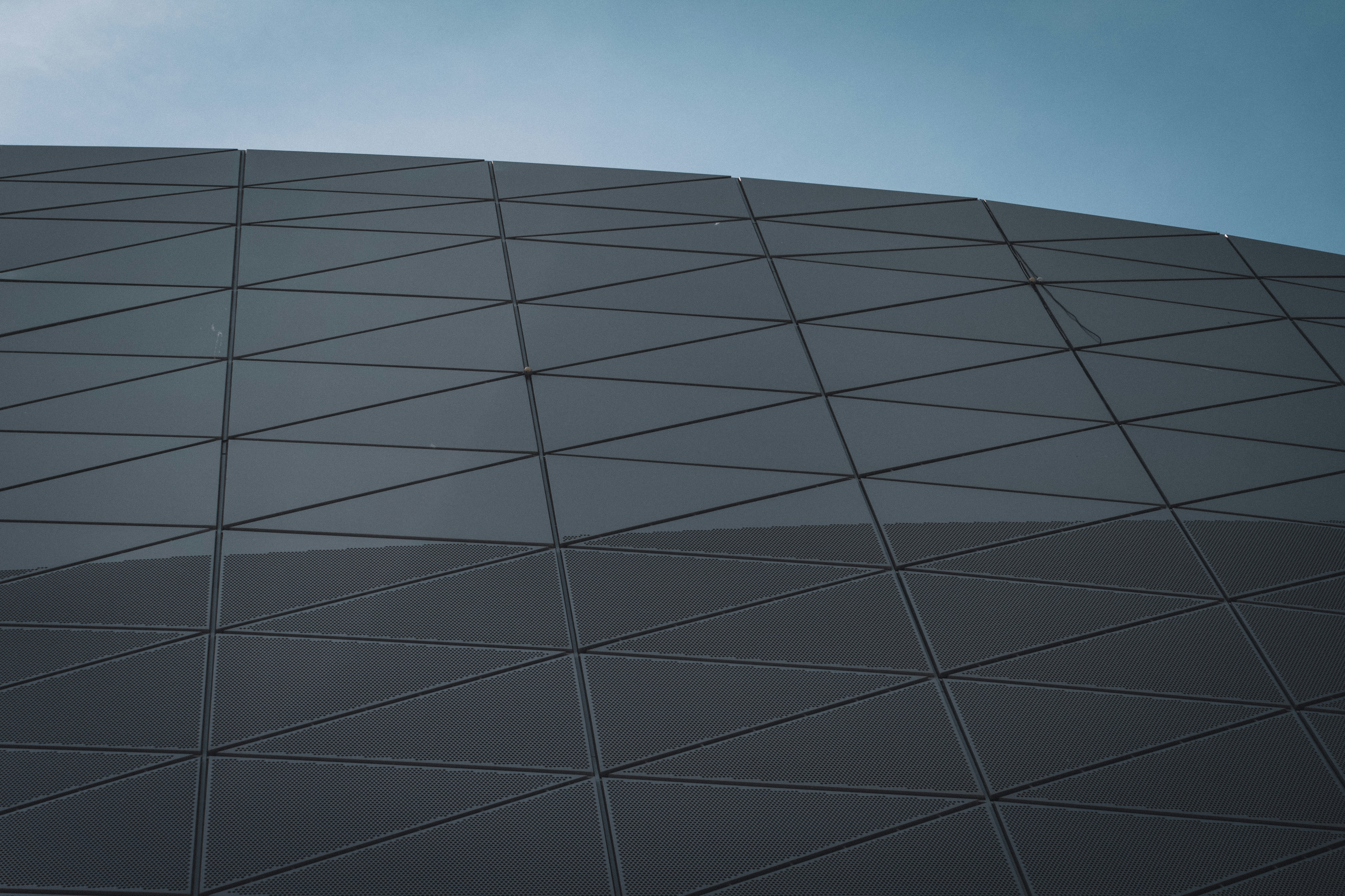 Close-up of a modern building facade showcasing a series of geometric patterns and textures. The interplay of light and shadow enhances the architectural design.