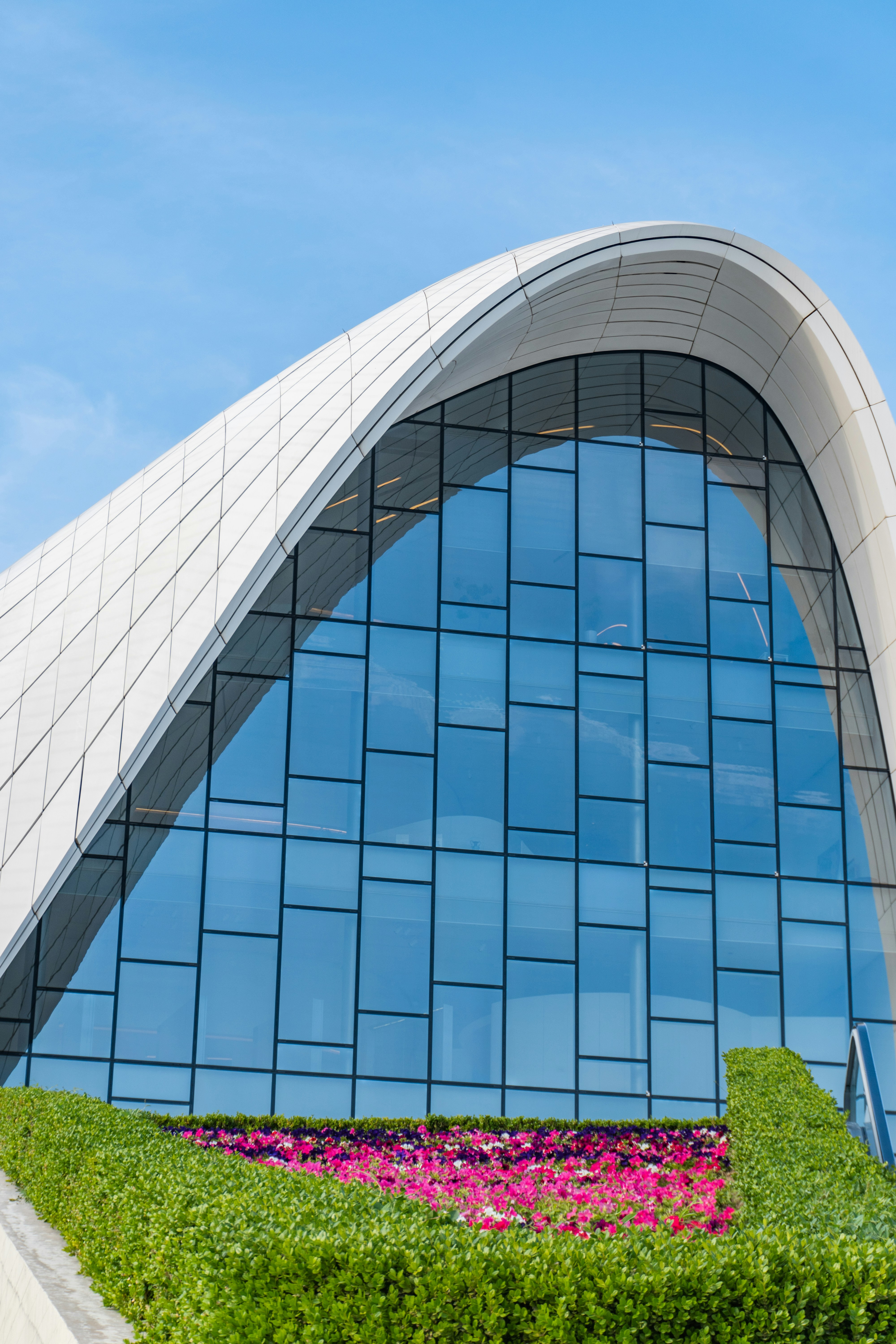 Arc of Blue Glass: A Modern Facade Framed by Greenery and Pink Blooms