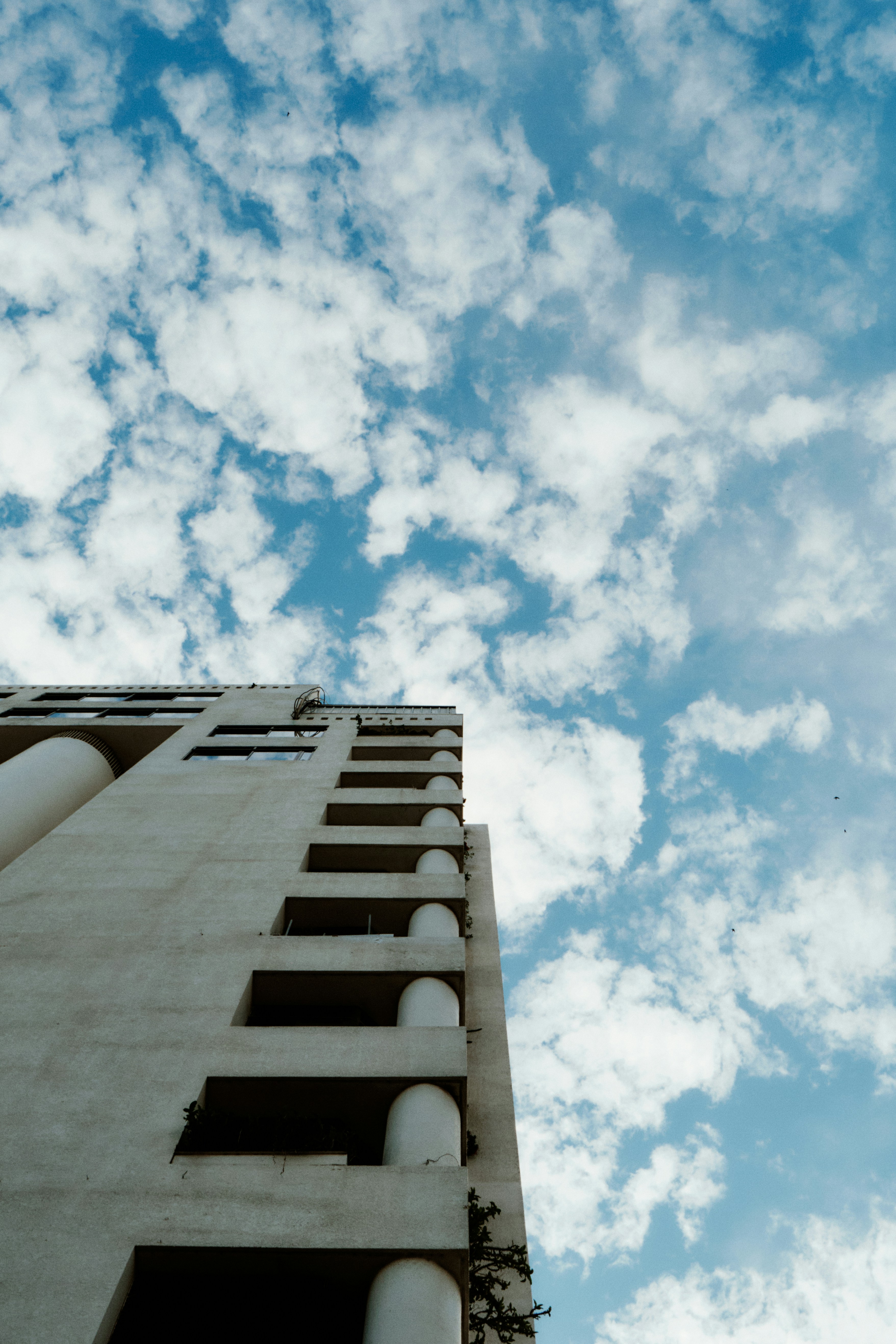 Modern building with prominent columns reaching towards a dynamic sky filled with scattered clouds.