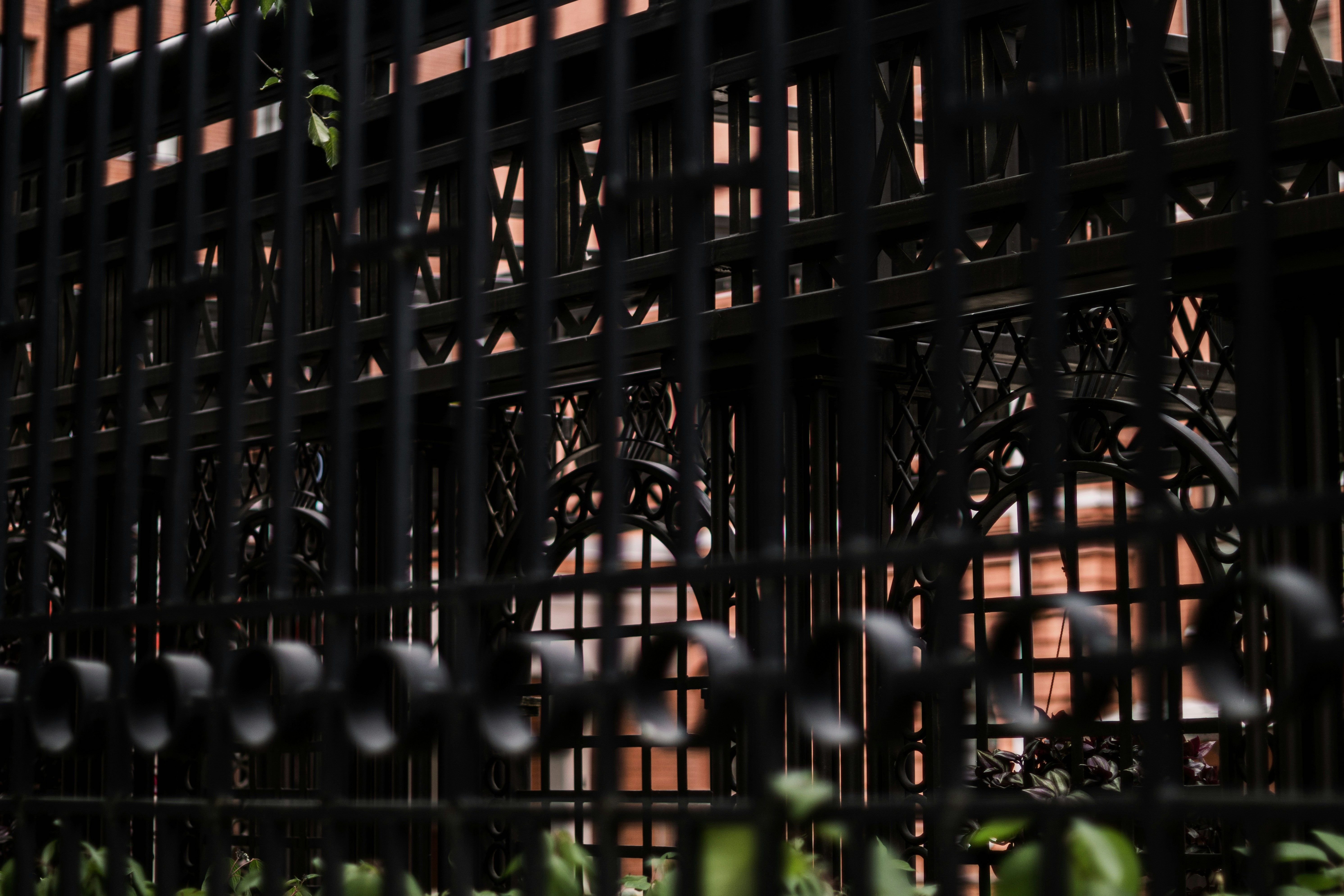 Ornate metalwork of a decorative fence partially obscuring a brick wall, showcasing intricate patterns and textures.