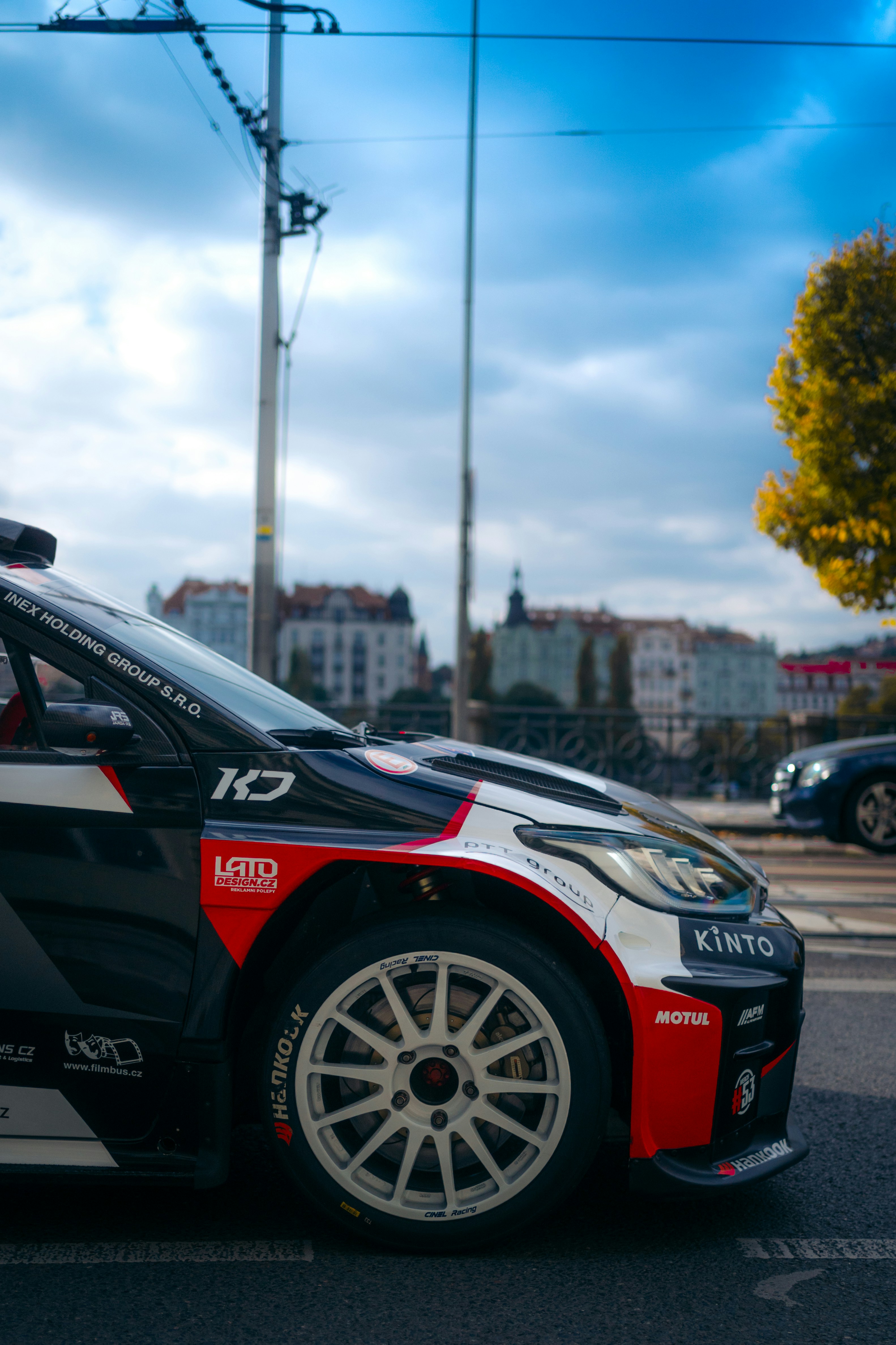 Grit and Gloss: Close-up of a race car's front-left amid an urban backdrop