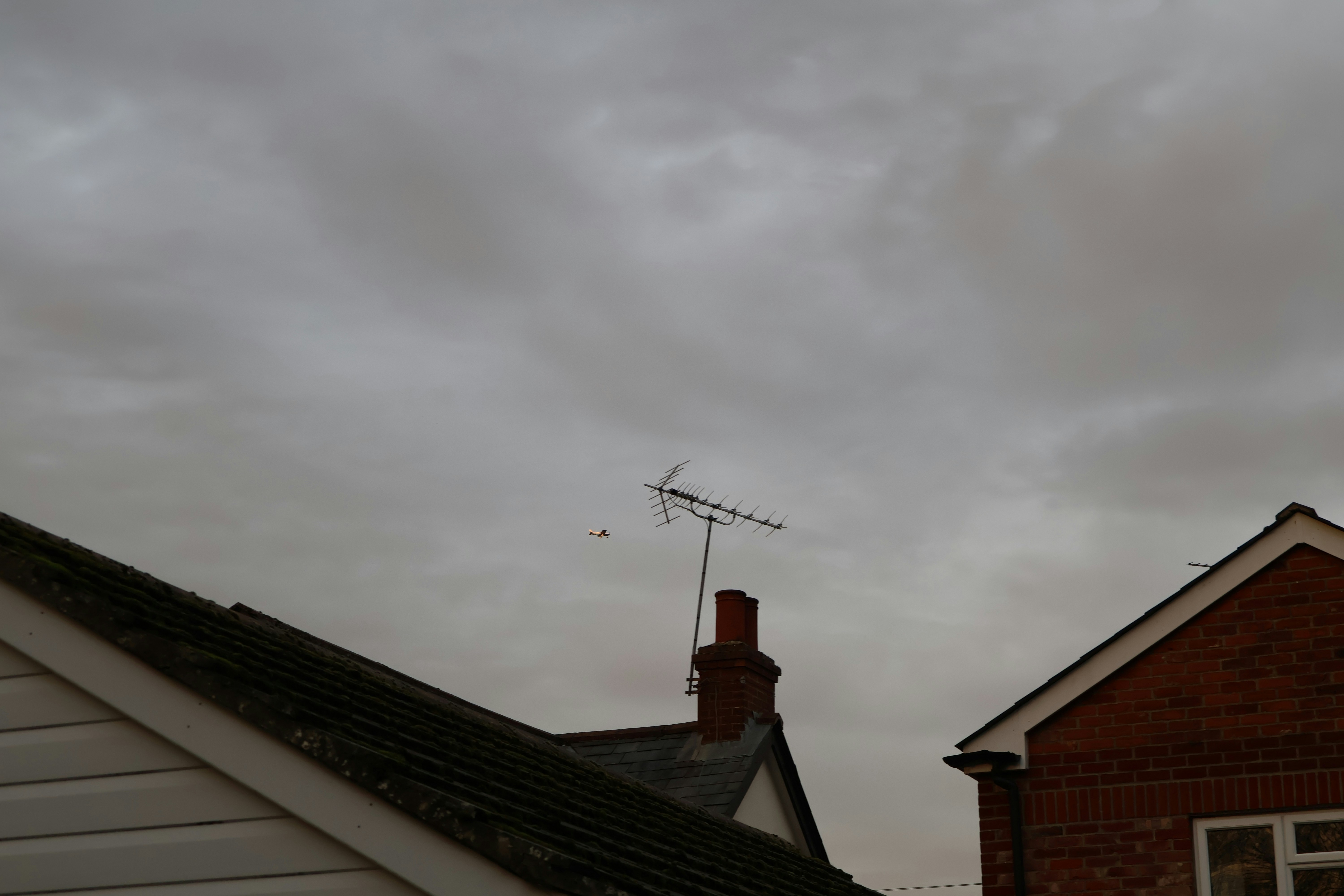 Overcast Rooftop Sentinel: Antenna on a Brick Chimney