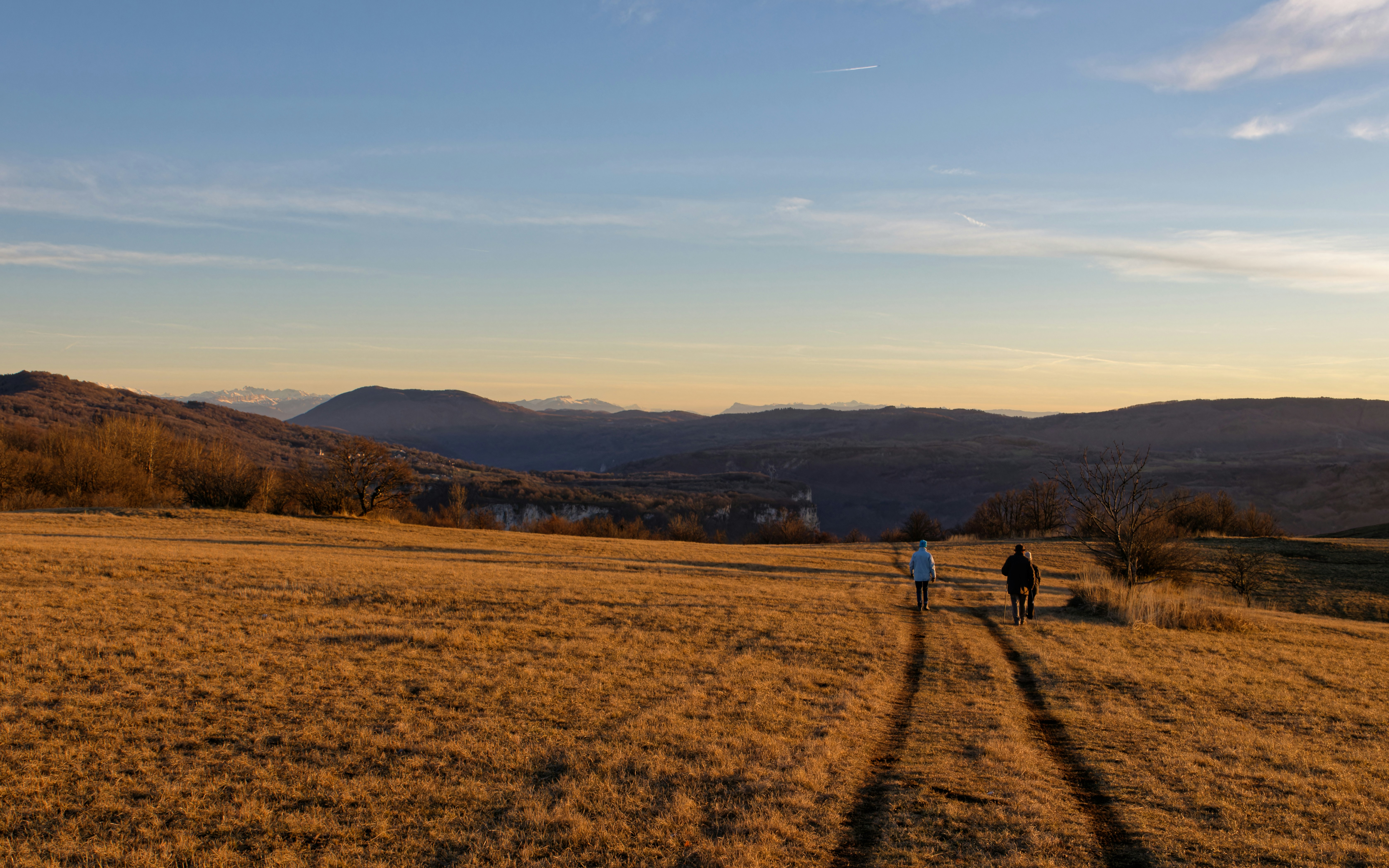 Golden Hour Trek: Two Figures Crossing a Sunlit Prairie Toward a Distant Range