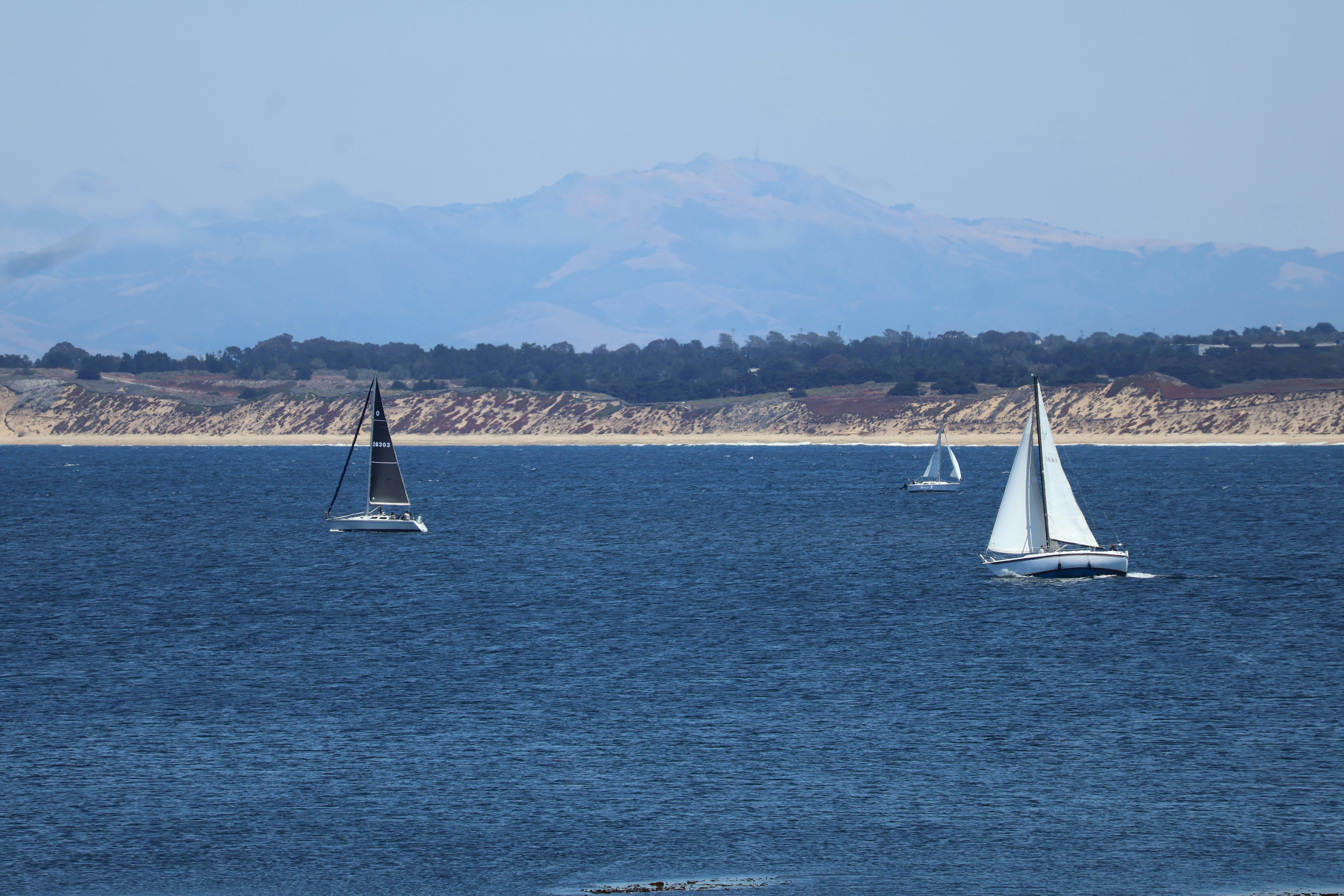 Two Sails in a Quiet Blue Bay, Distant Mountains Framing the Scene