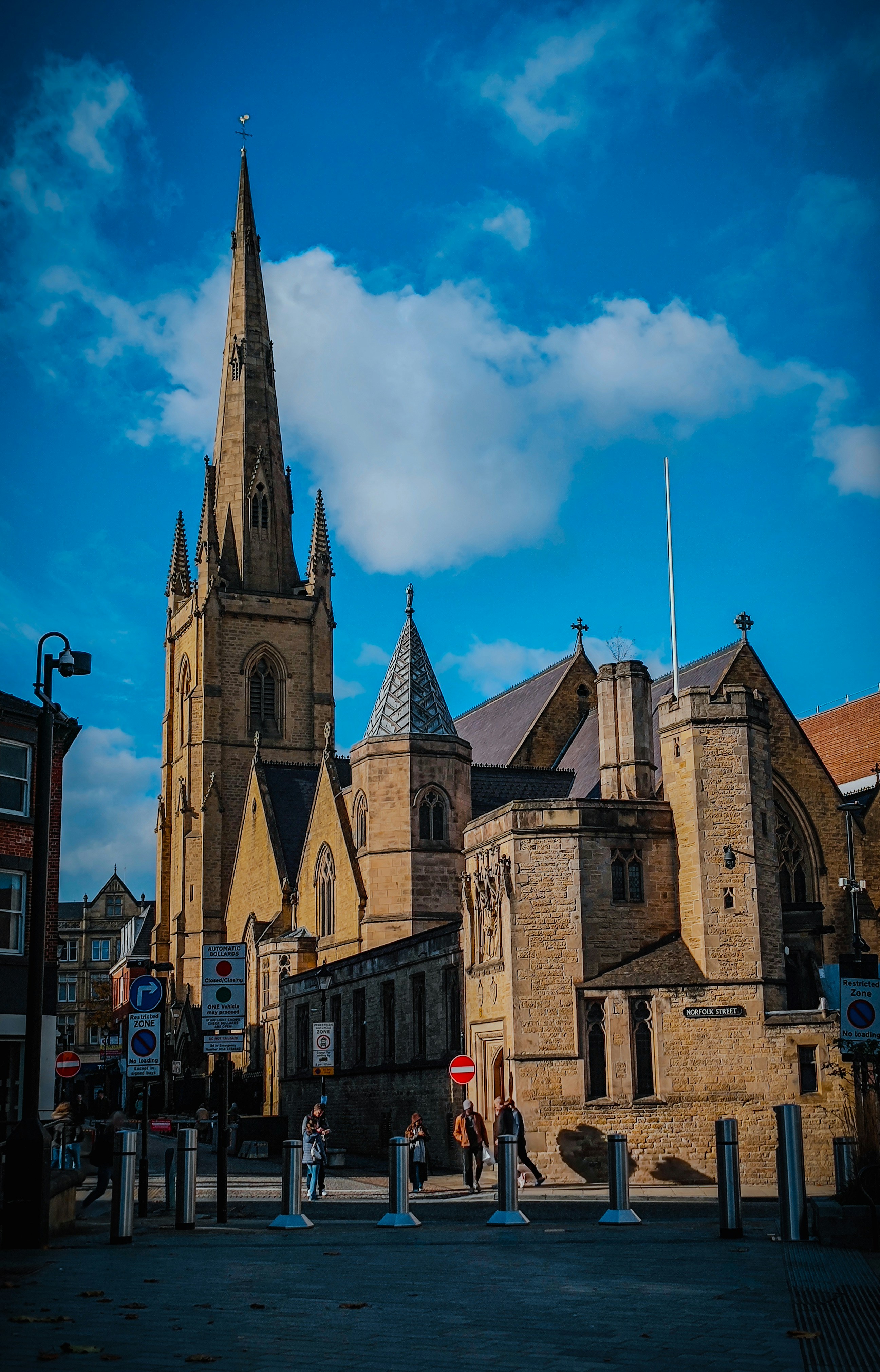 A stunning view of a historic Gothic-style church under a bright blue sky in Sheffield, England. The sharp spire, stone details, and warm sunlight create a timeless urban scene blending architecture and culture.