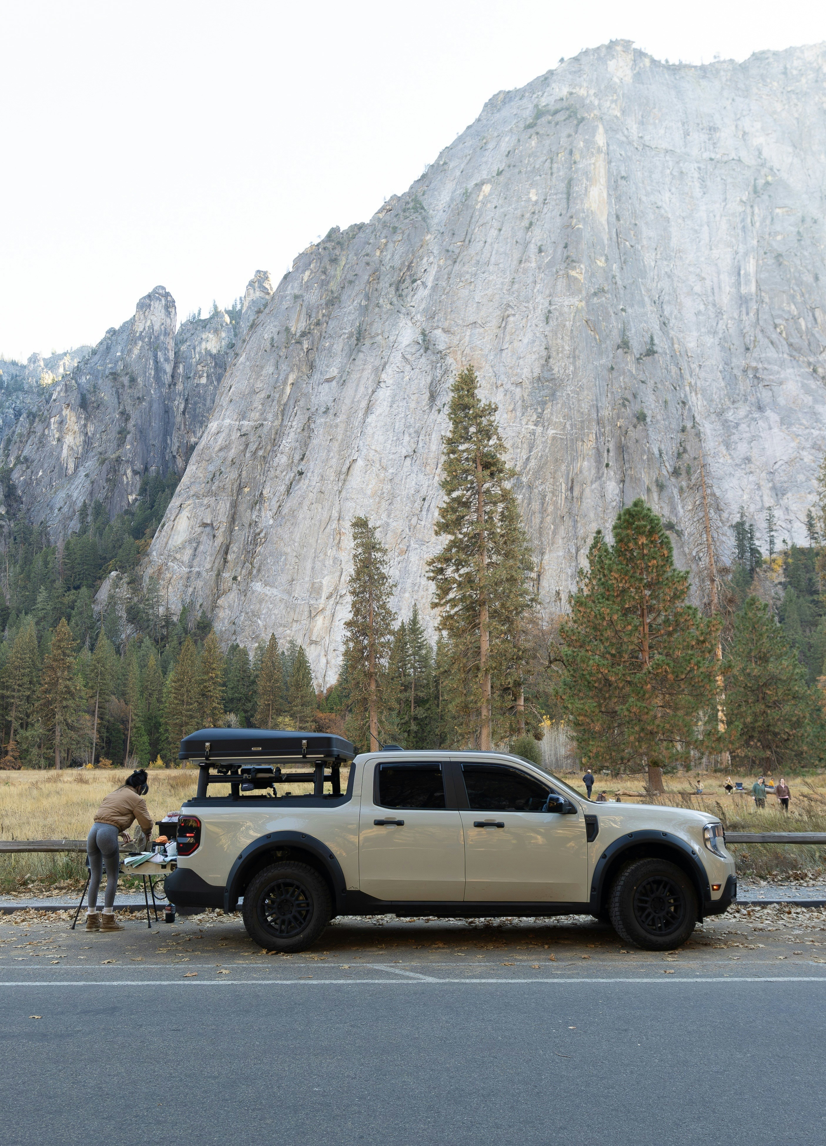 Person setting up camp next to truck with mountain backdrop