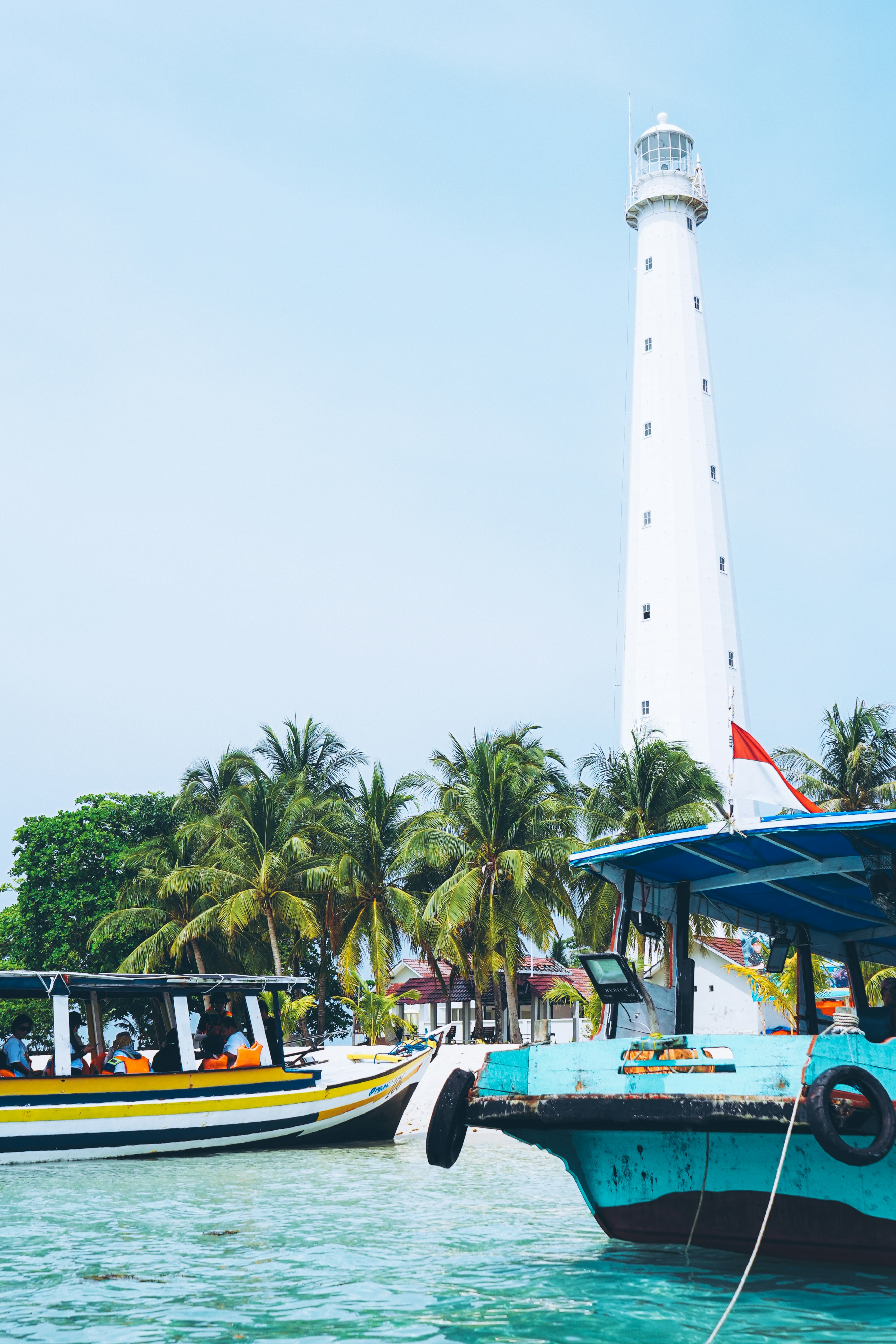 Lighthouse Over Turquoise Harbor: Palm-Fringed Shoreline with Colorful Boats