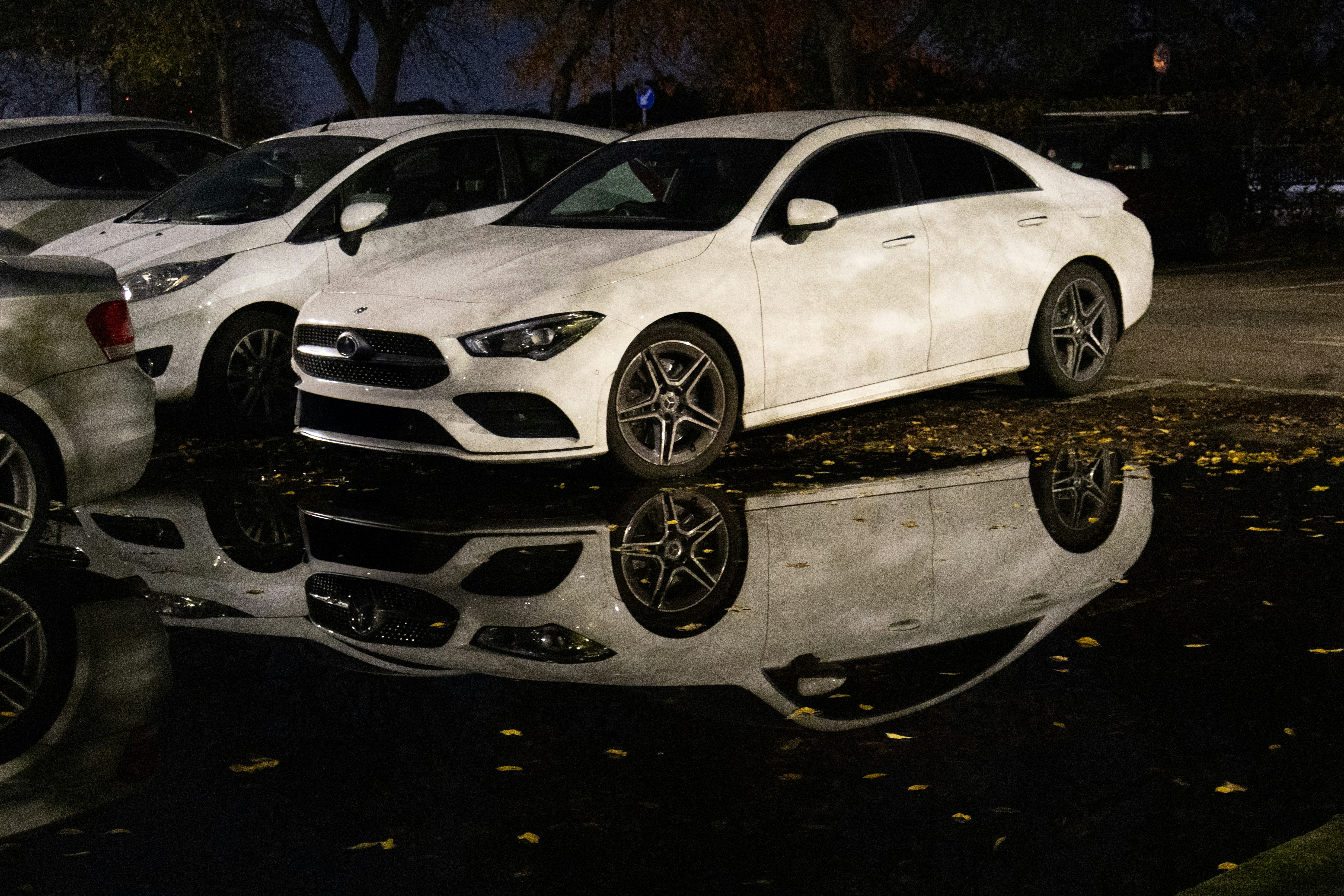 Twin Reflections: A White Sedan Anchored by a Rain-Slick Parking Lot