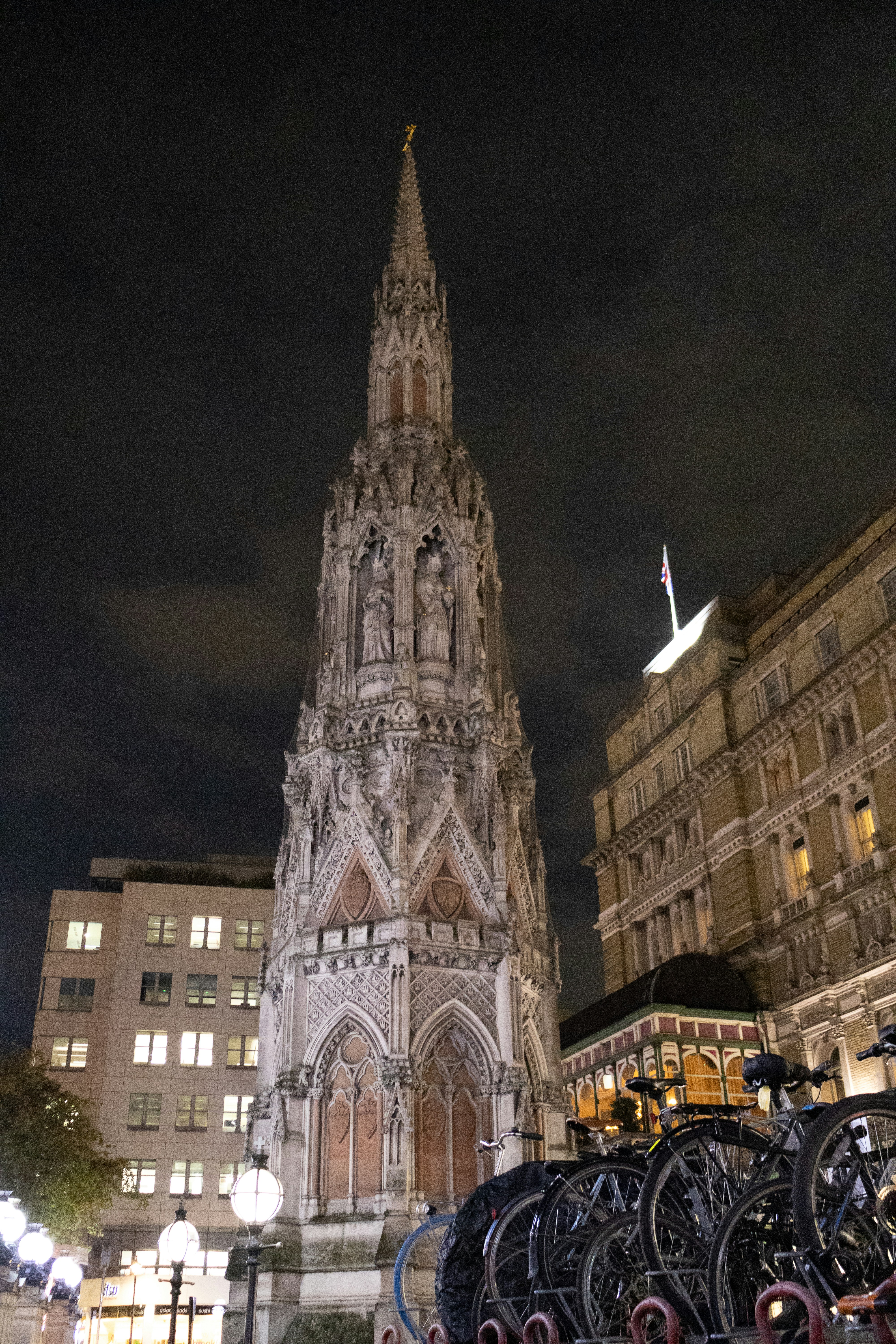Ornate gothic monument at night with buildings.
