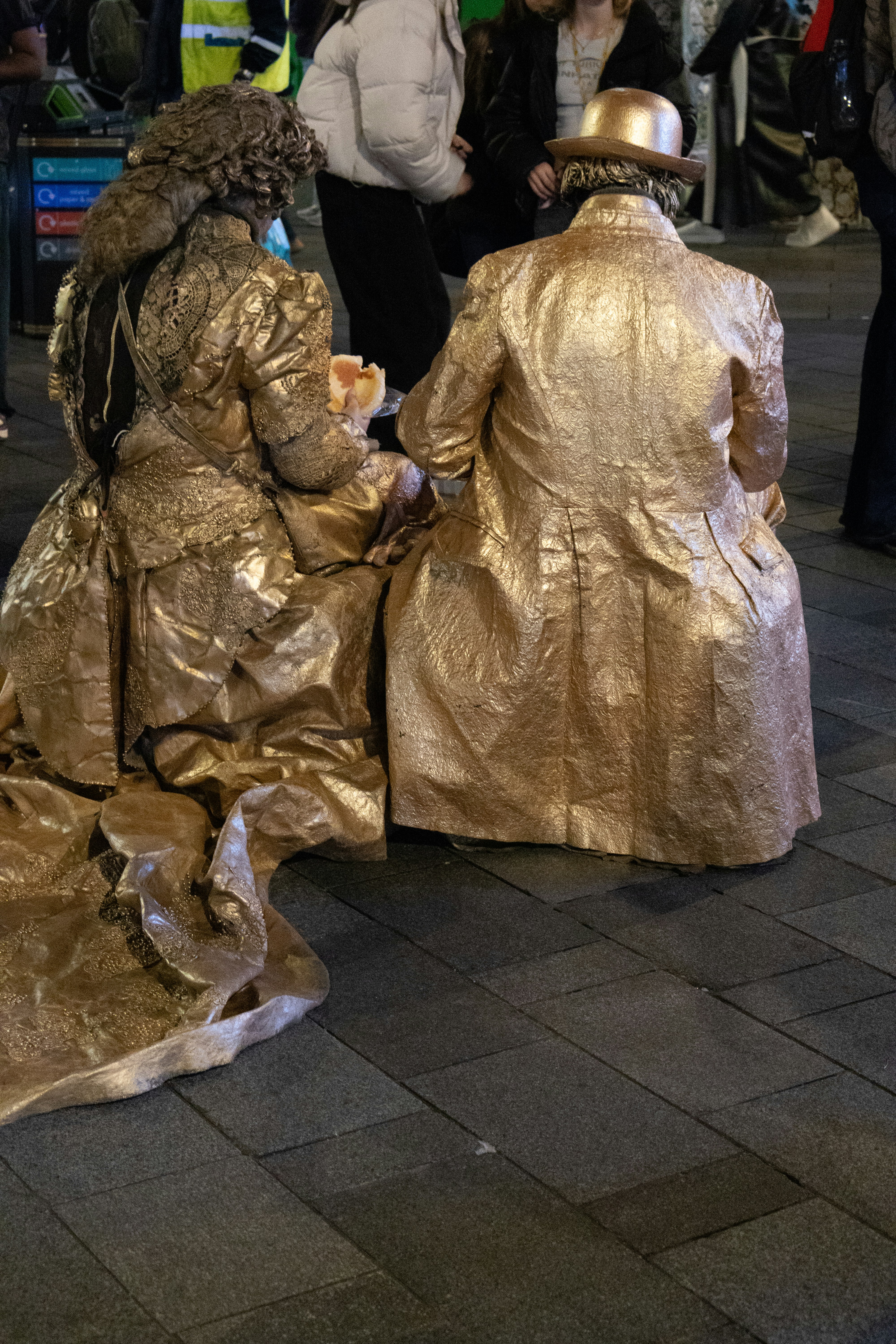 Urban Glint: Two Gold-Clad Figures Resting in a Busy Square