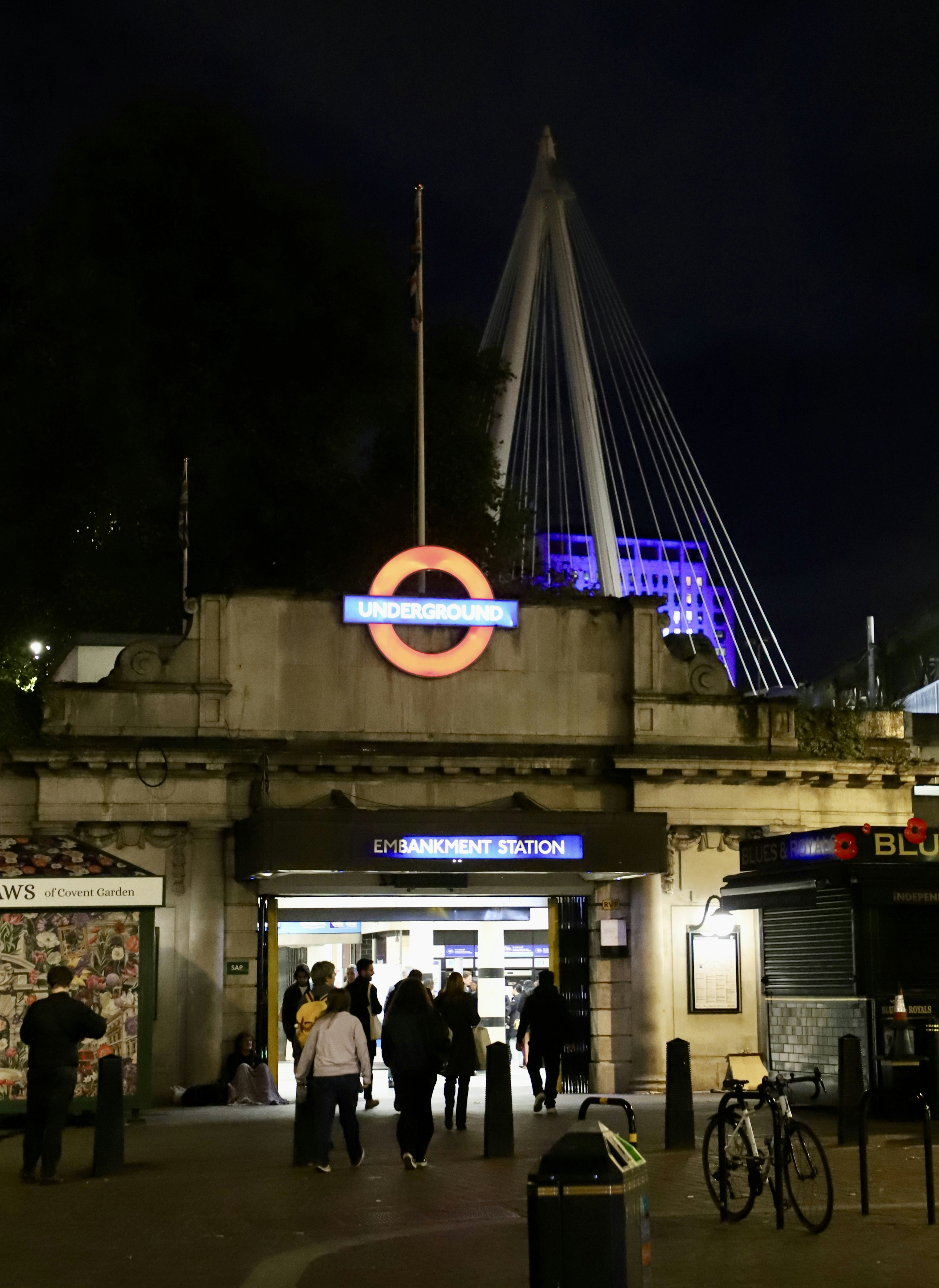 Underground Roundel Over Embankment: Night Entrance Beneath a Neon Bridge