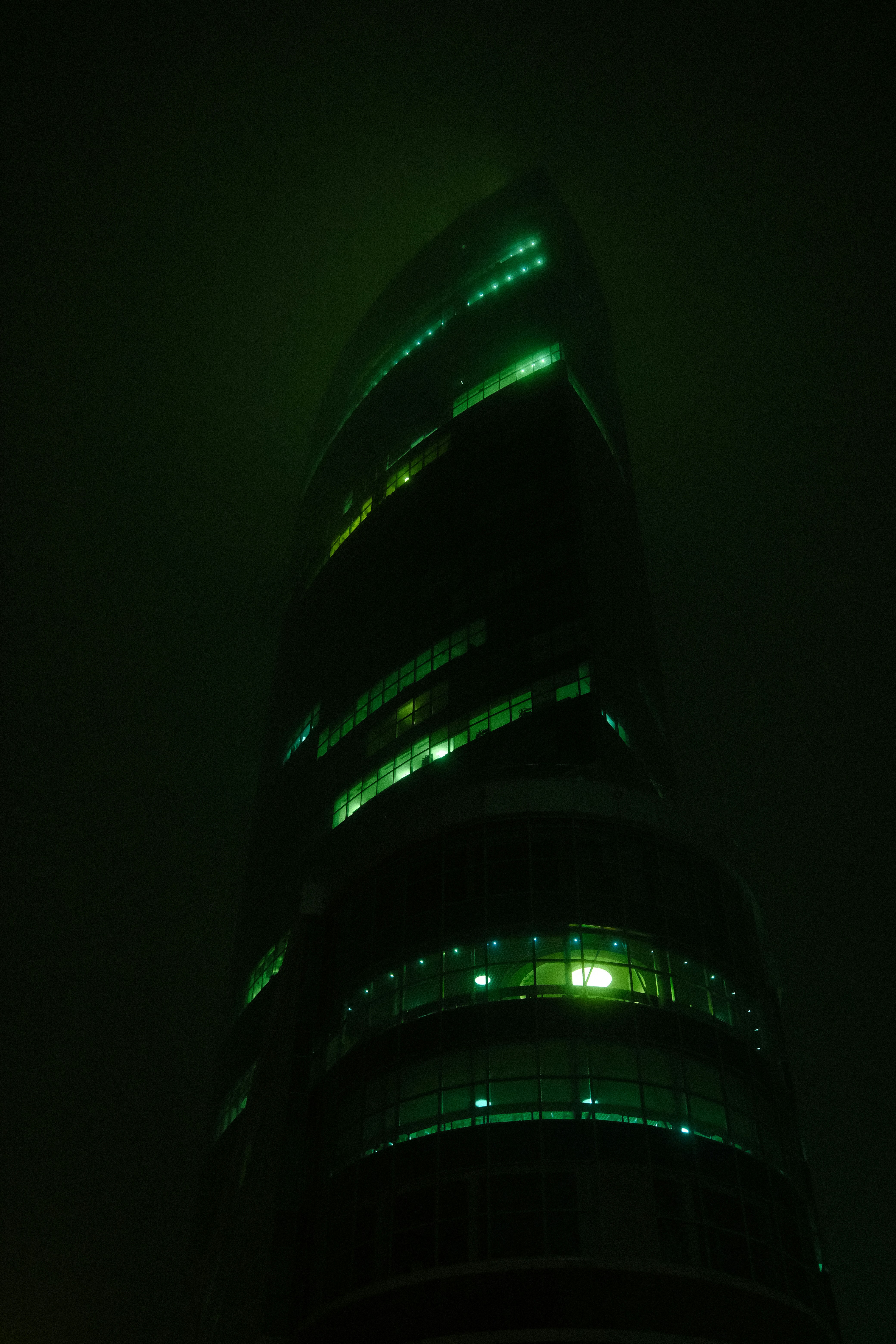 Verdant Facade: The Green-Lit Curved Tower at Night