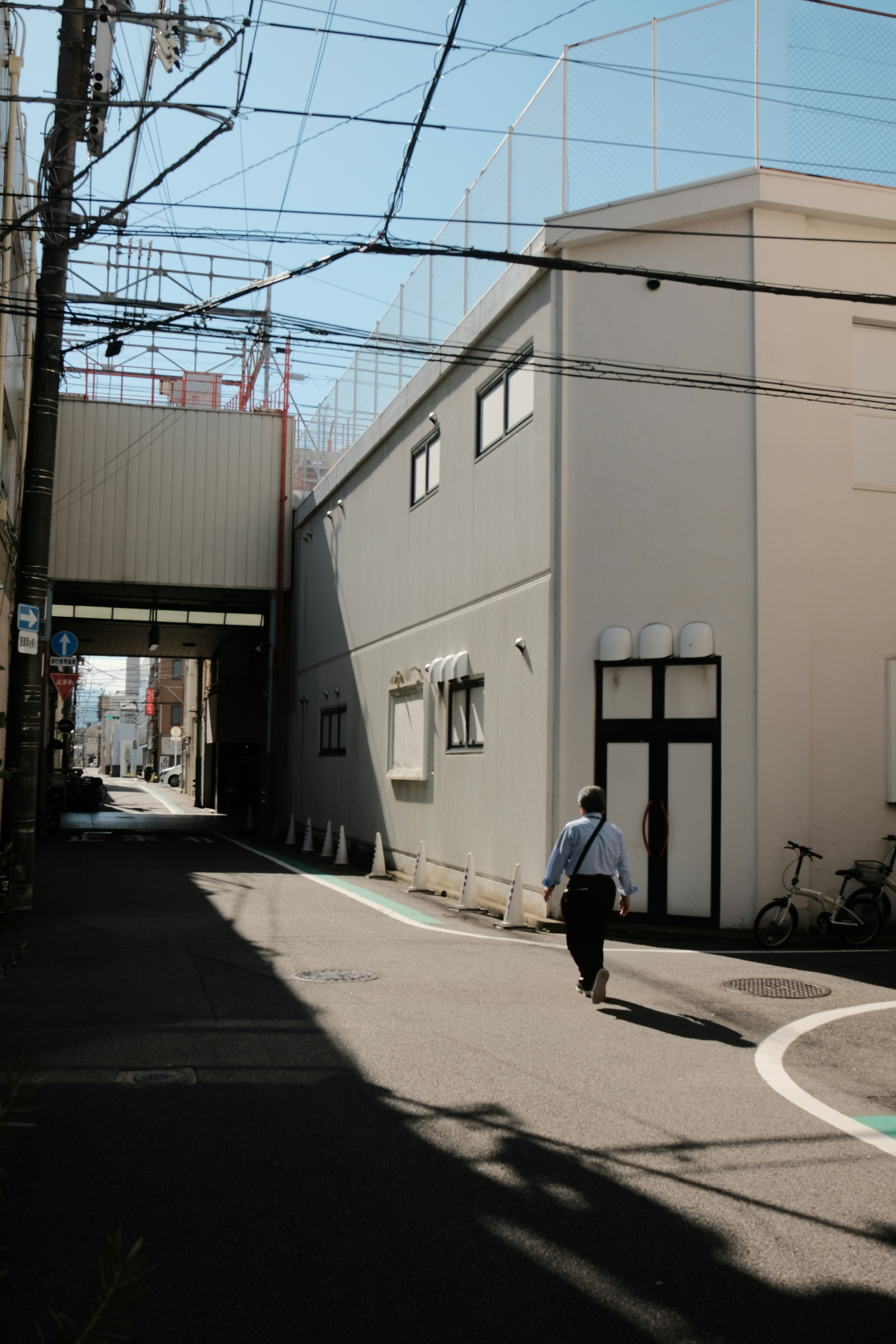 Lone Walker in a Sunlit Alley Under a Web of Wires