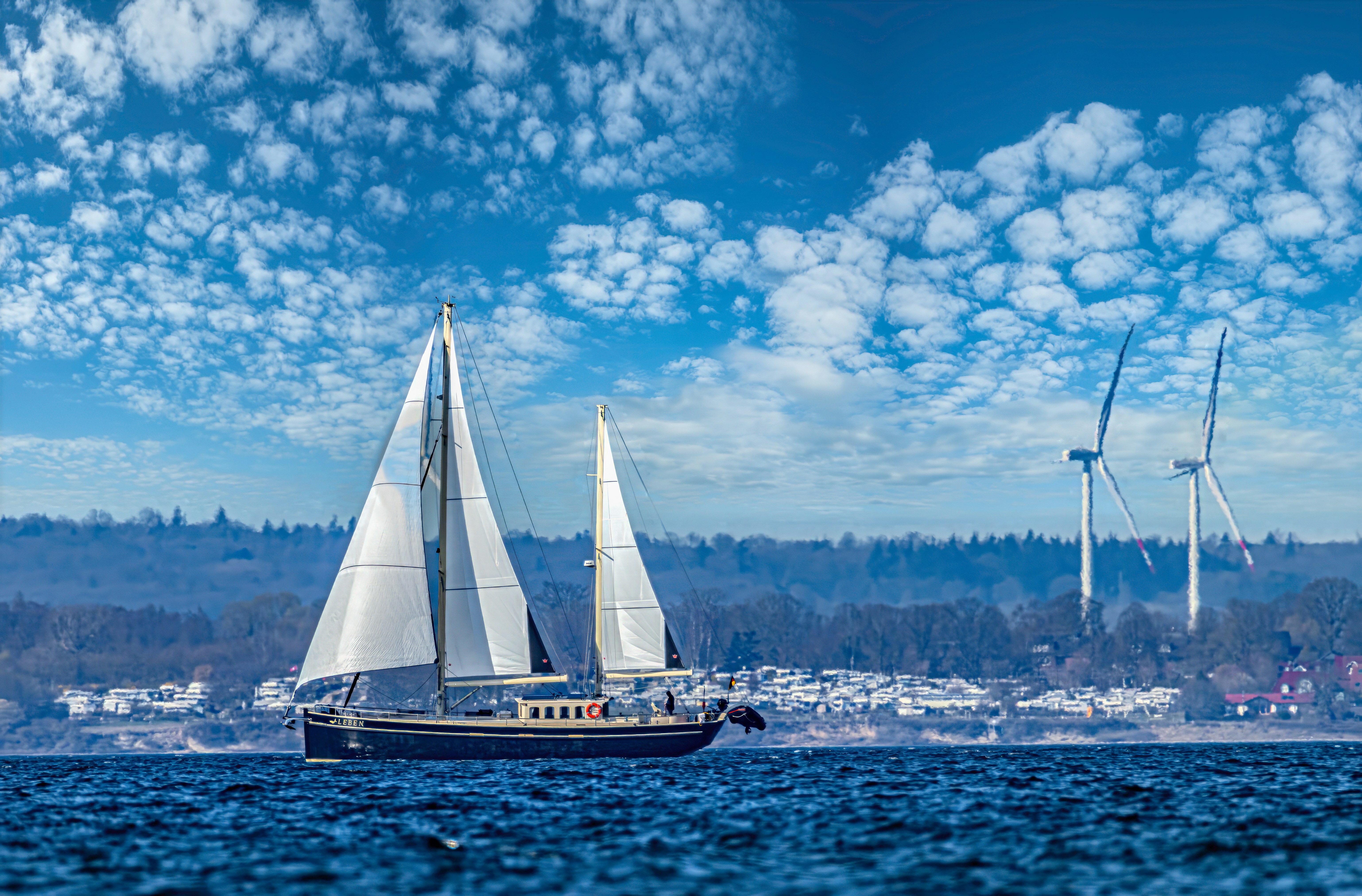 Blue-Sailed Passage: A Schooner Navigates Calm Seas Before a Wind-Turbine Horizon
