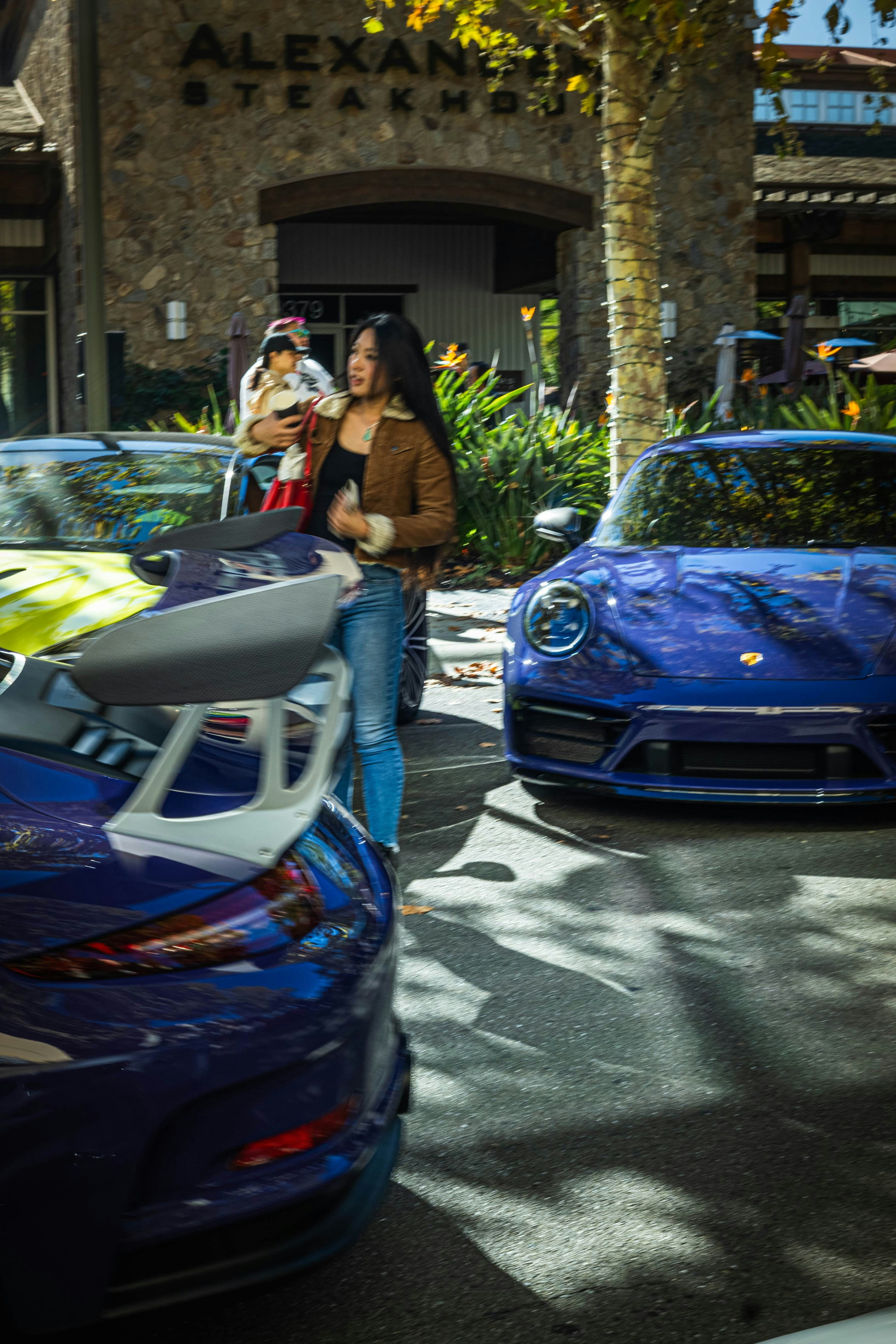 Blue Porsche Parade: A Woman Strolls Outside a Stone Steakhouse