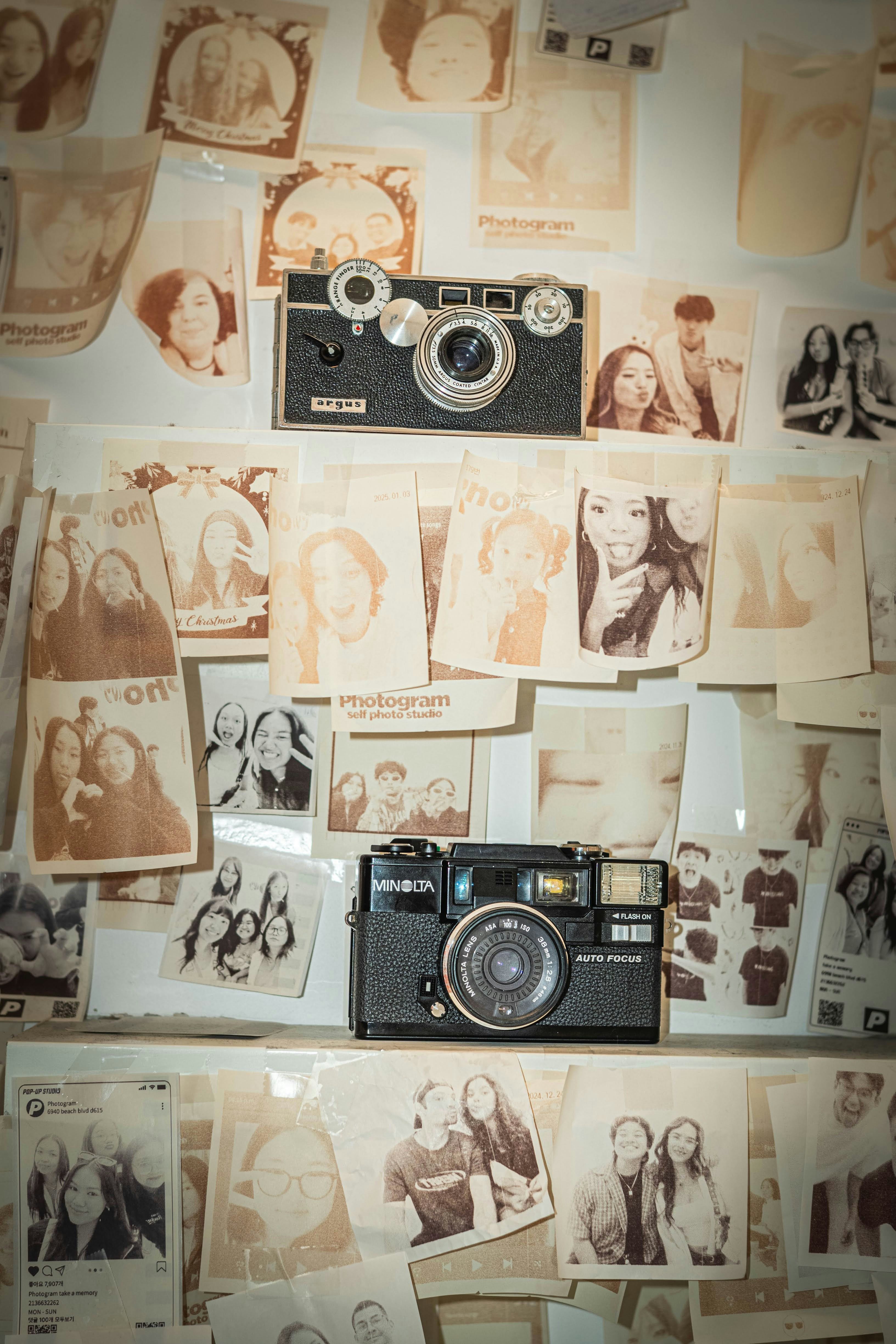 Sentinels of Snapshot History: Two Vintage Cameras Amid a Wall of Portraits