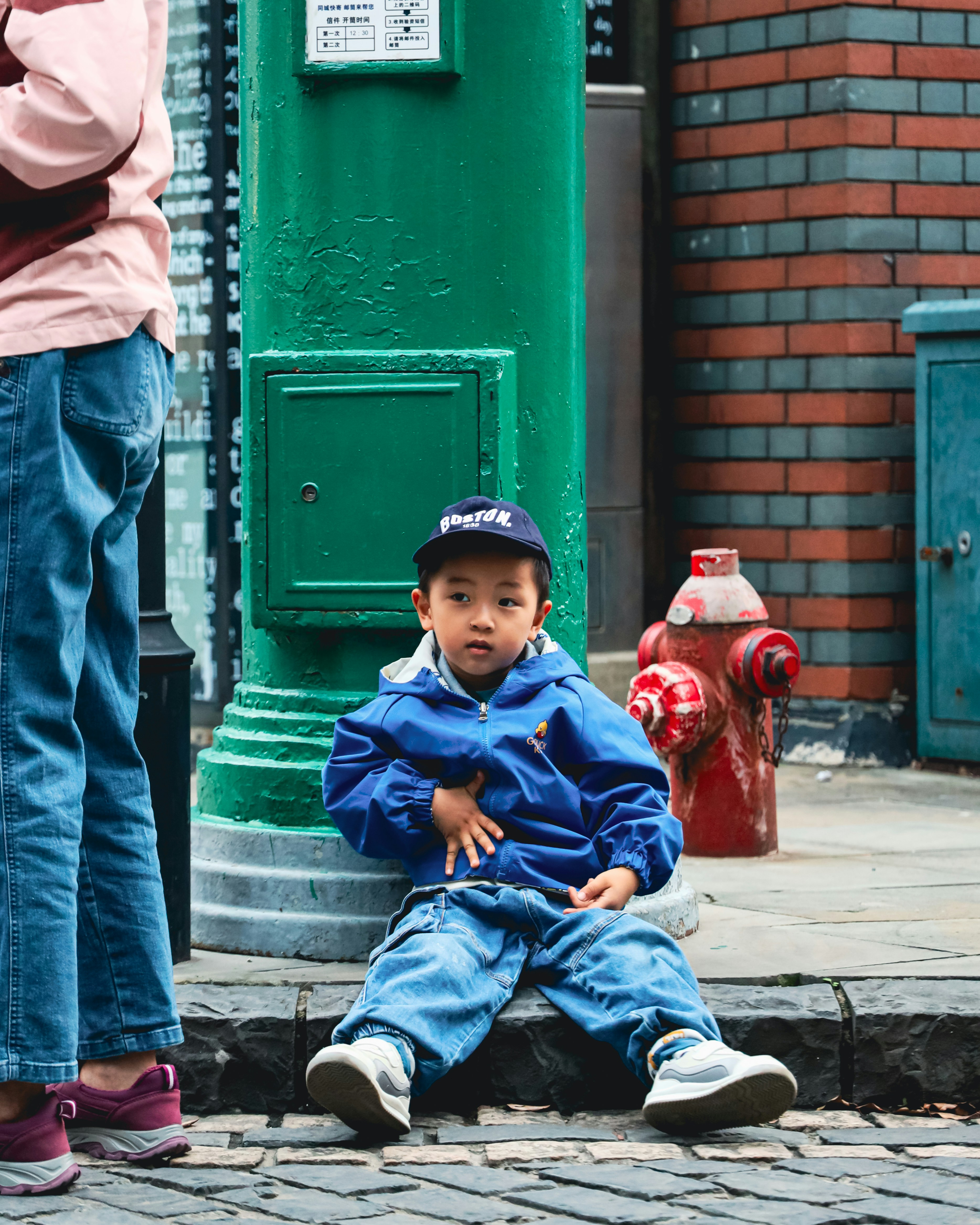 Young boy in blue jacket sits by green pole photo – Free China Image on ...