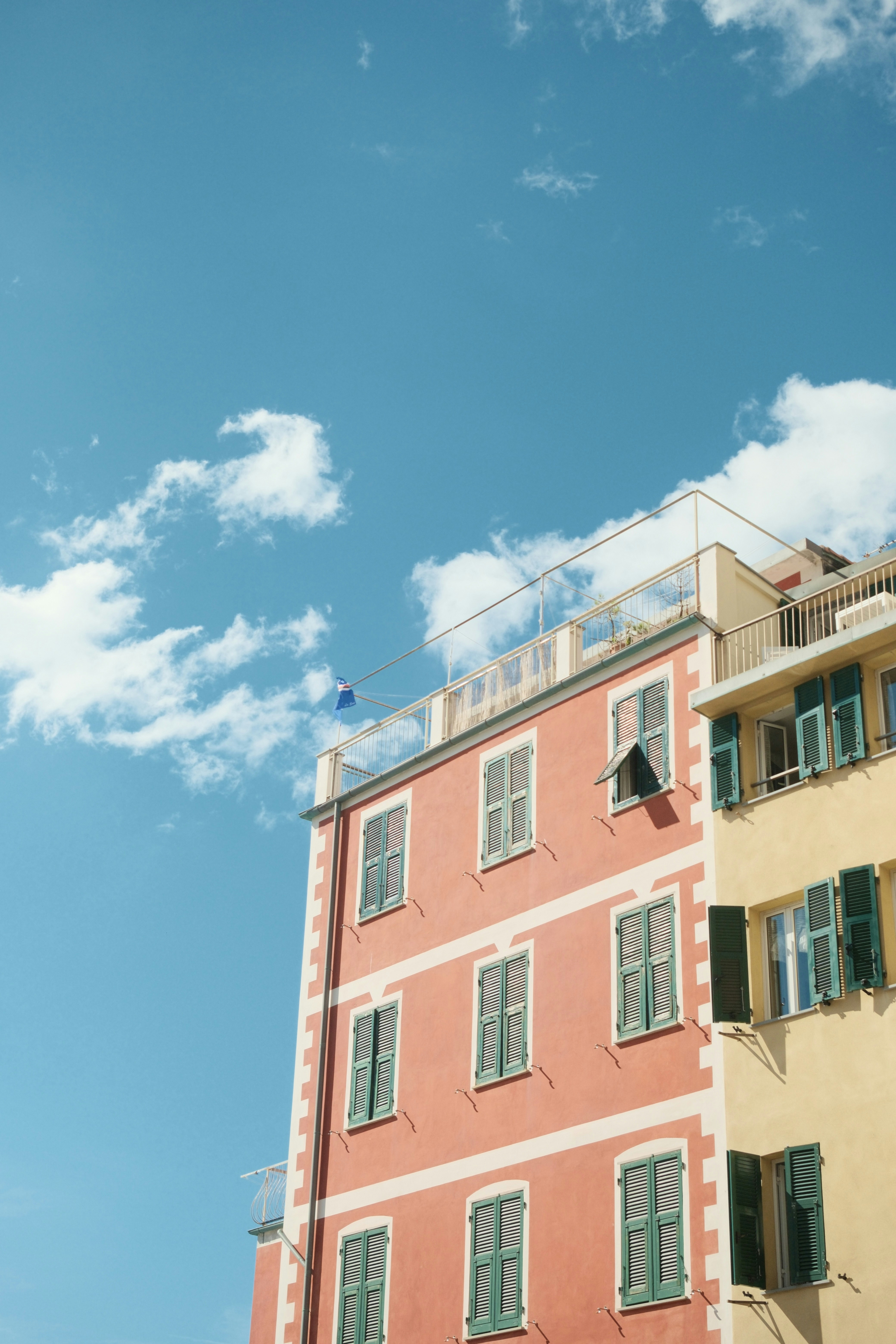 Sunlit Pink Facade with Green Shutters Under a Clear Cyan Sky
