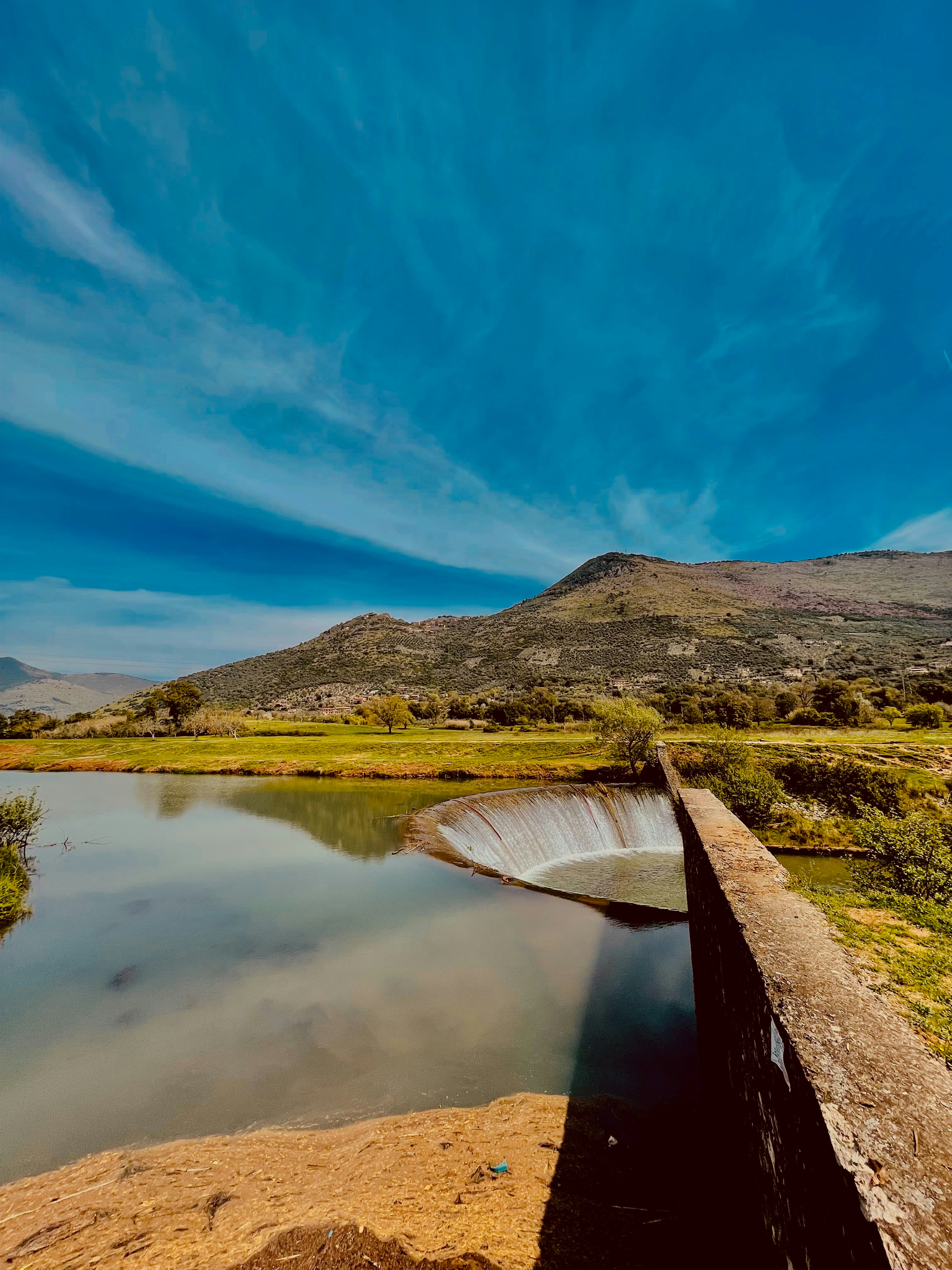 Edge of the Dam: A Quiet Valley River under a Wide Blue Sky