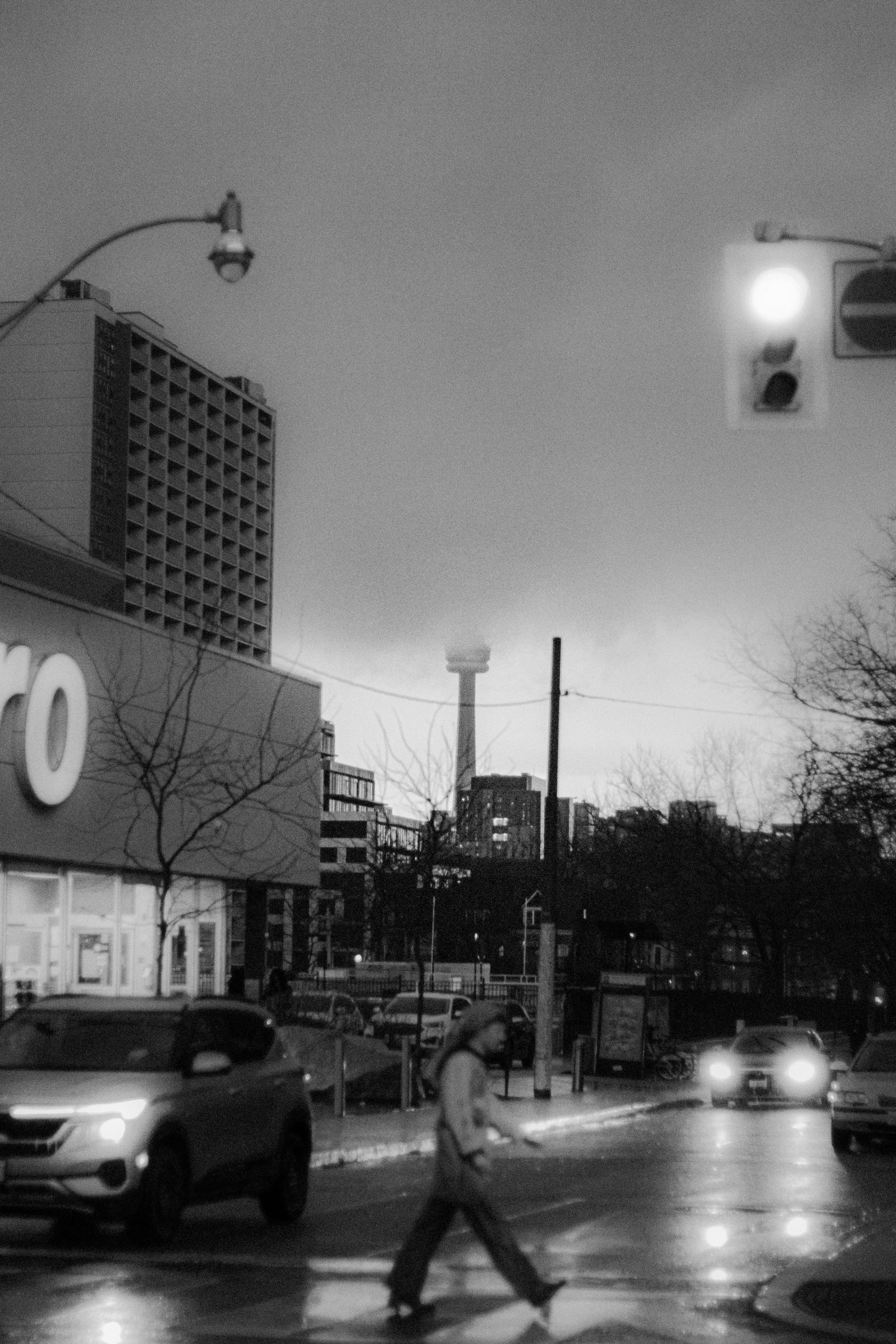 Monochrome Crossing: A lone pedestrian threads through a rain-slick urban intersection