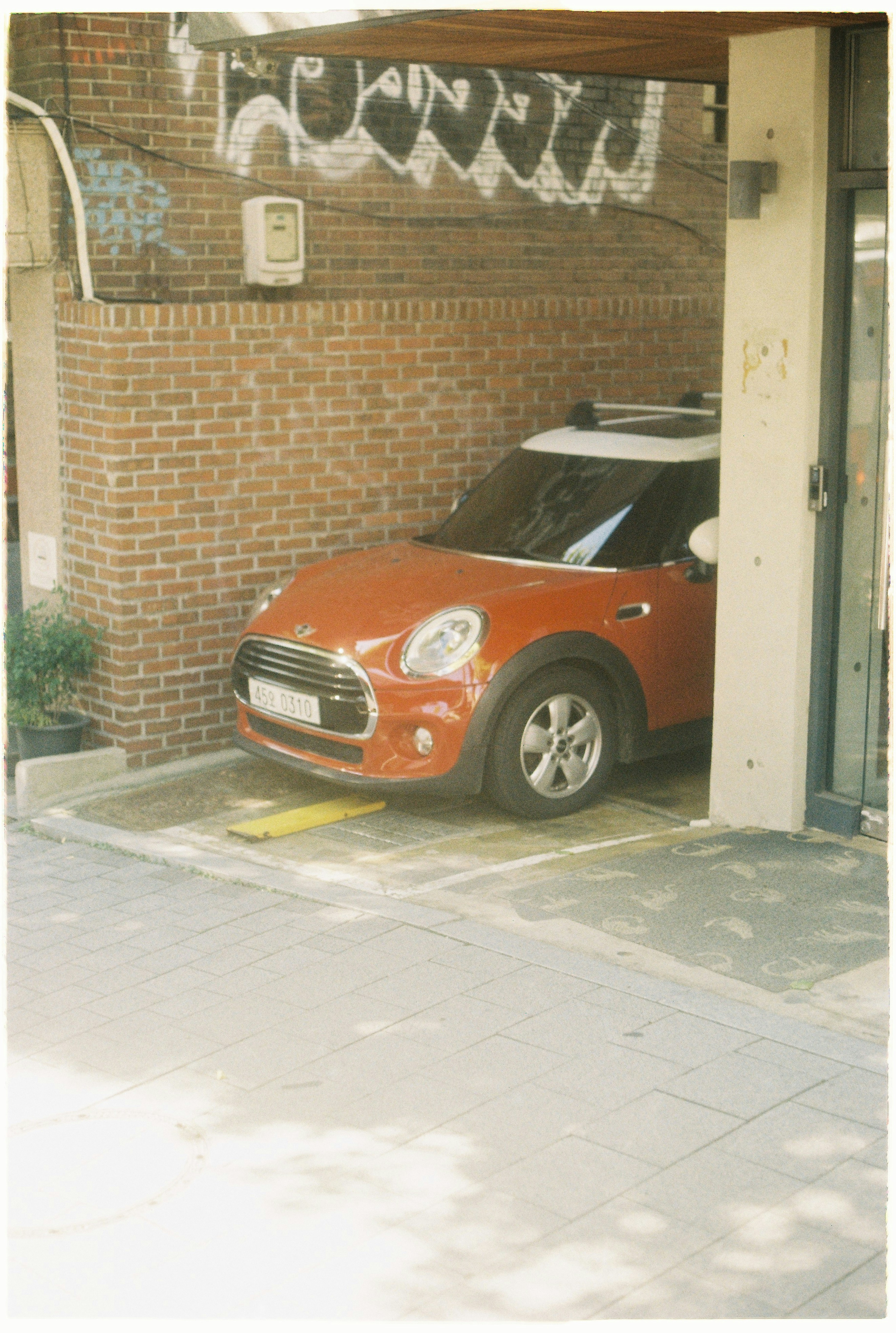Orange Mini in a Brick-Walled Parking Nook