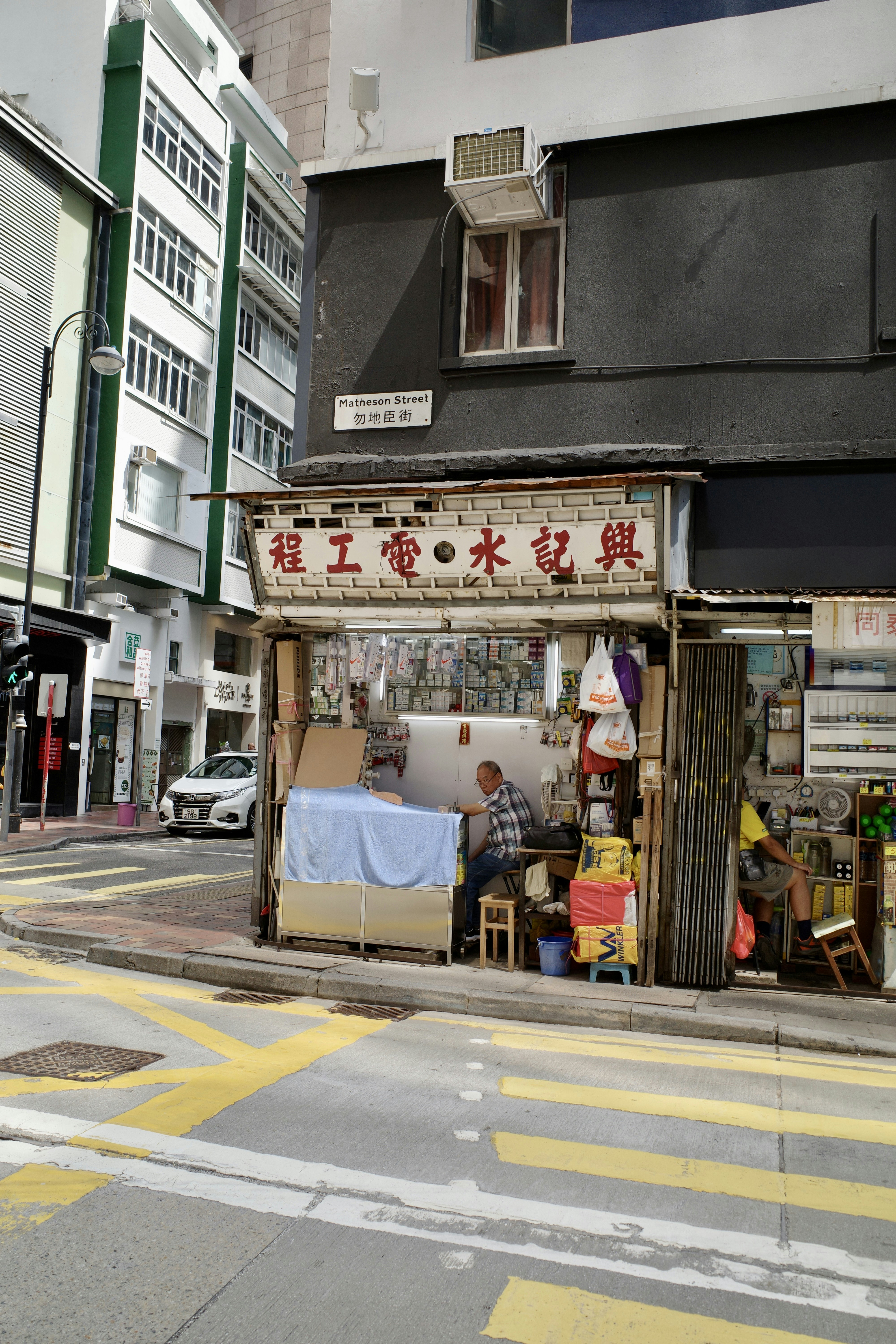 Man sitting at a small storefront on a city street. photo – Free Retail ...