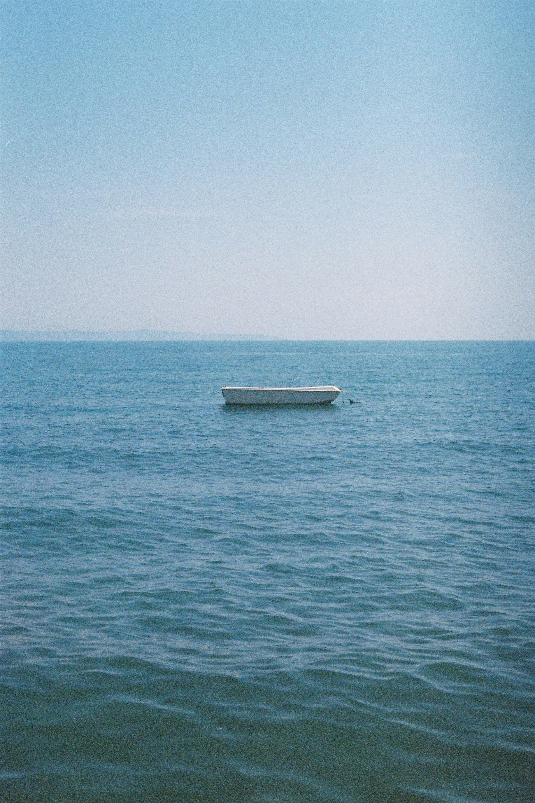 A small white boat floats on calm blue ocean water.