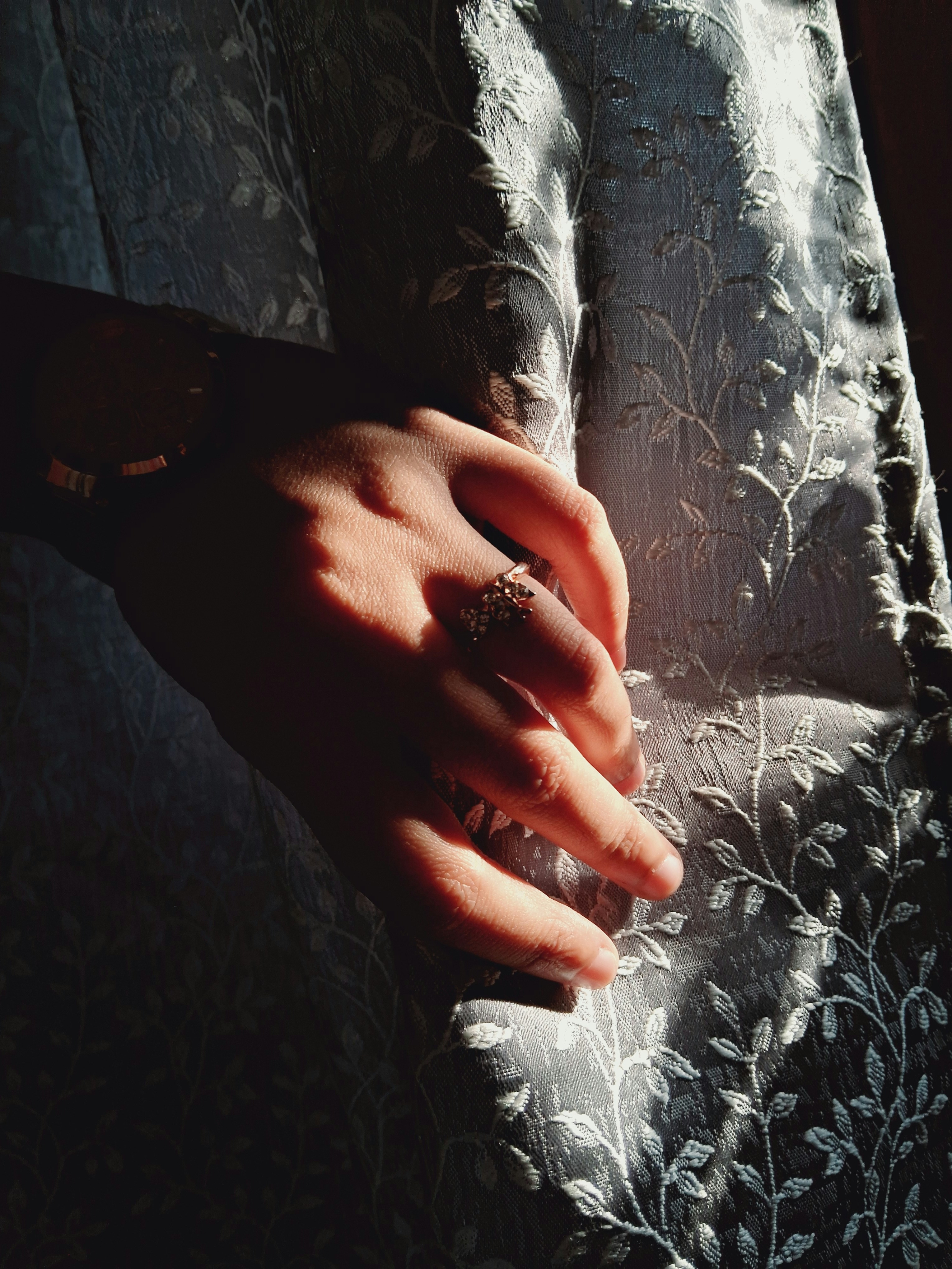 Woman's hand with ring in sunlight on fabric.