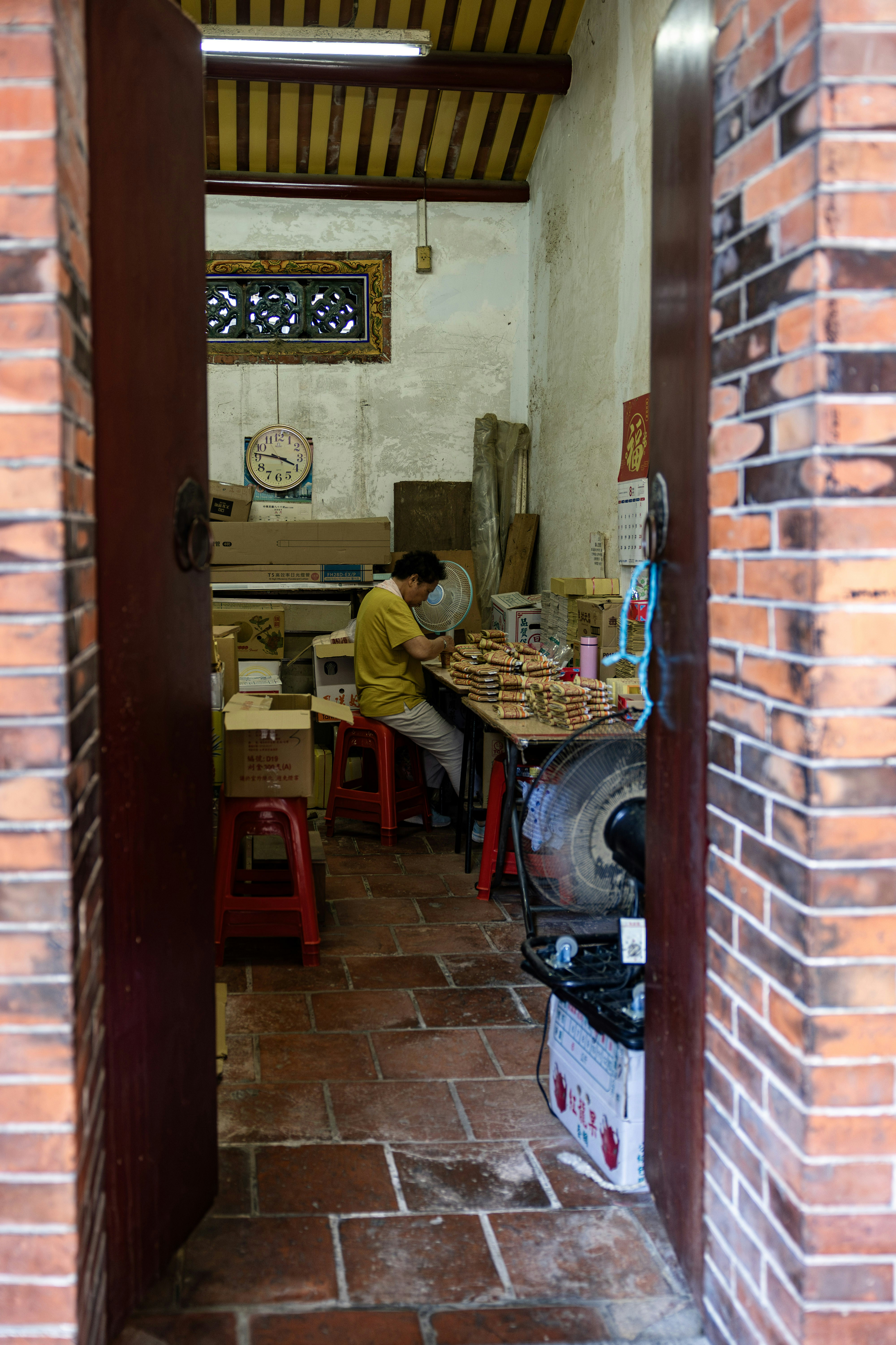 Brick-Walled Workshop: Yellow-Shirt Craftsman Among Stacks of Boxes