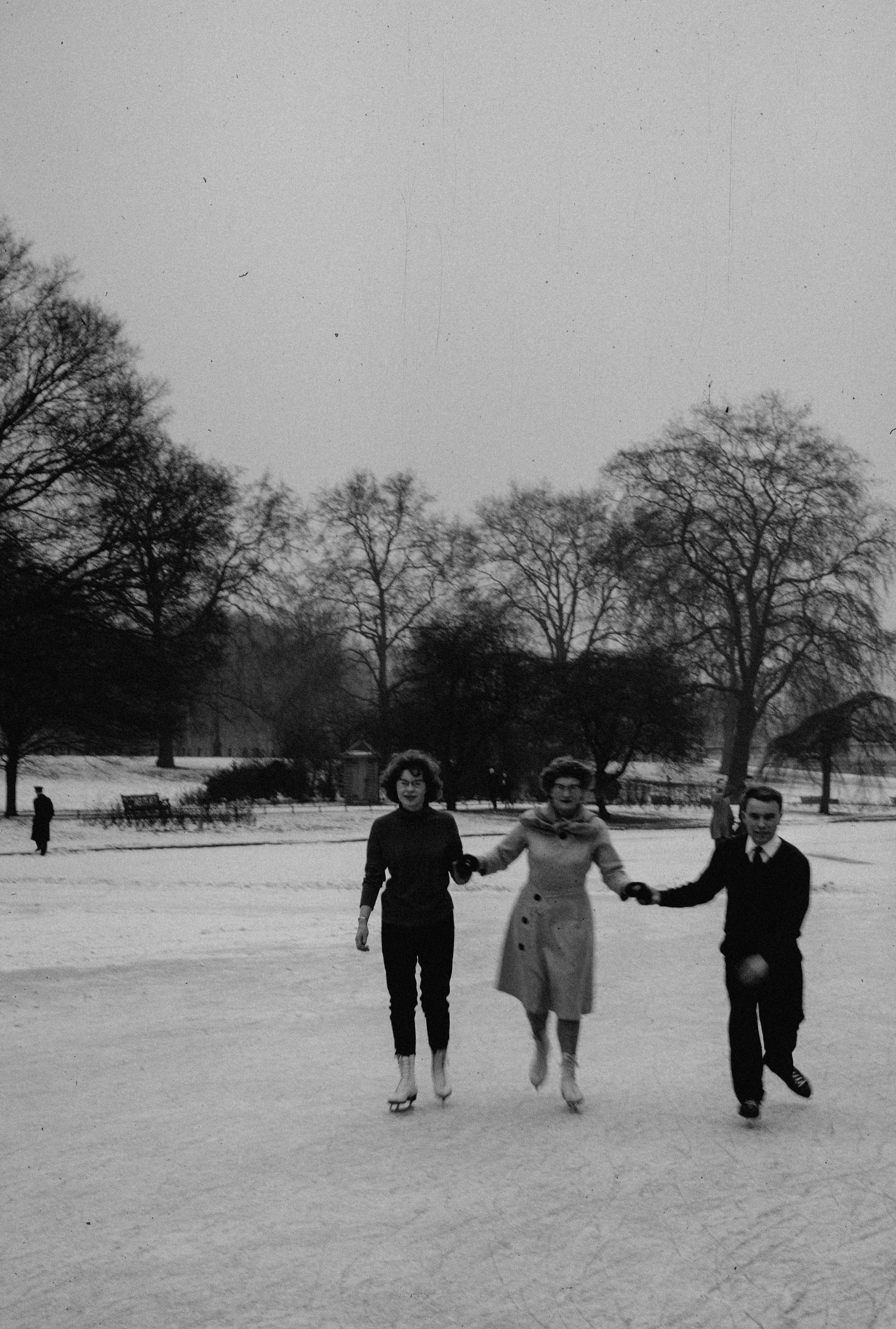 Three people holding hands ice skating in a park.