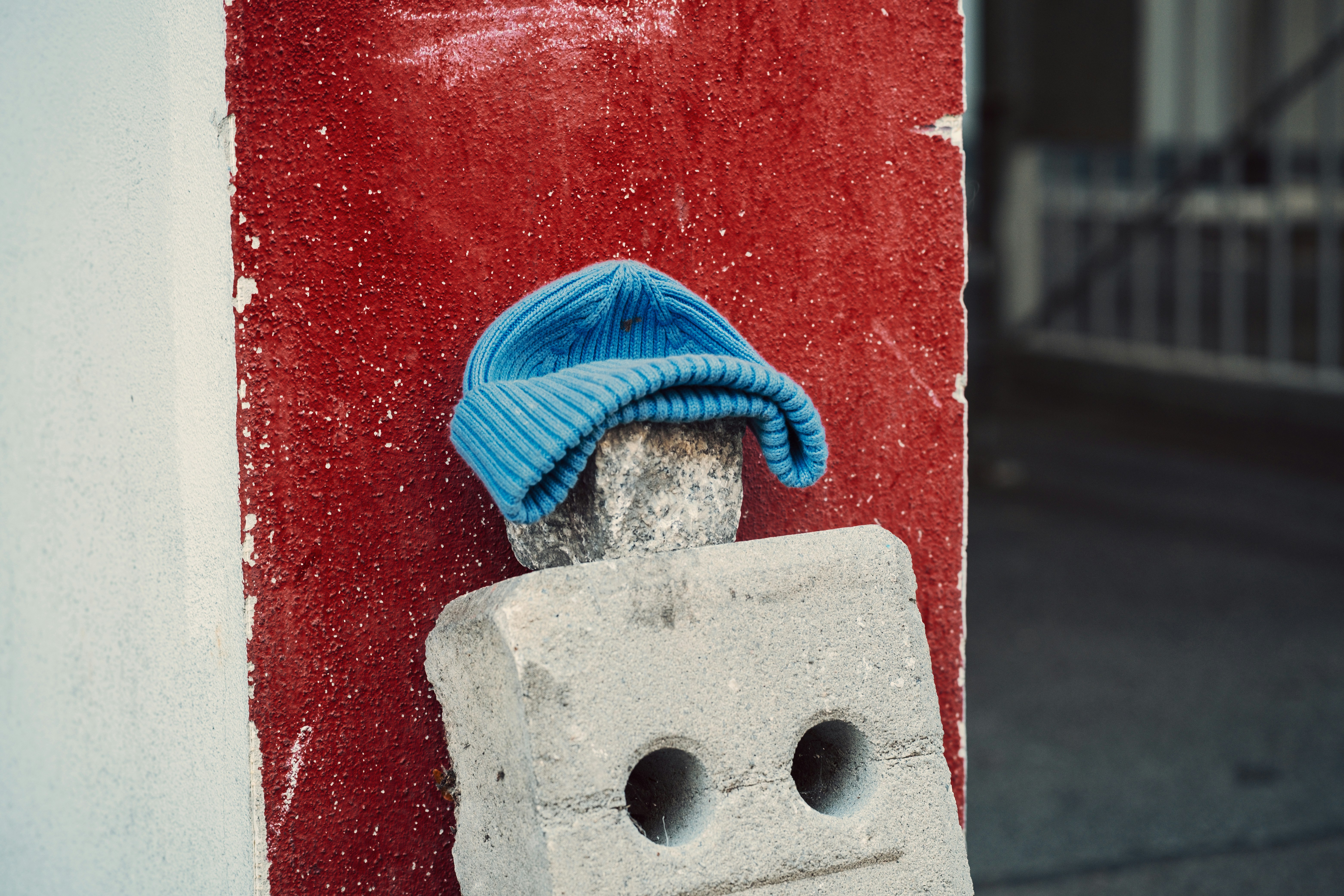 Blue Beanie on a Concrete Block: A Quiet Urban Portrait Against a Red Panel