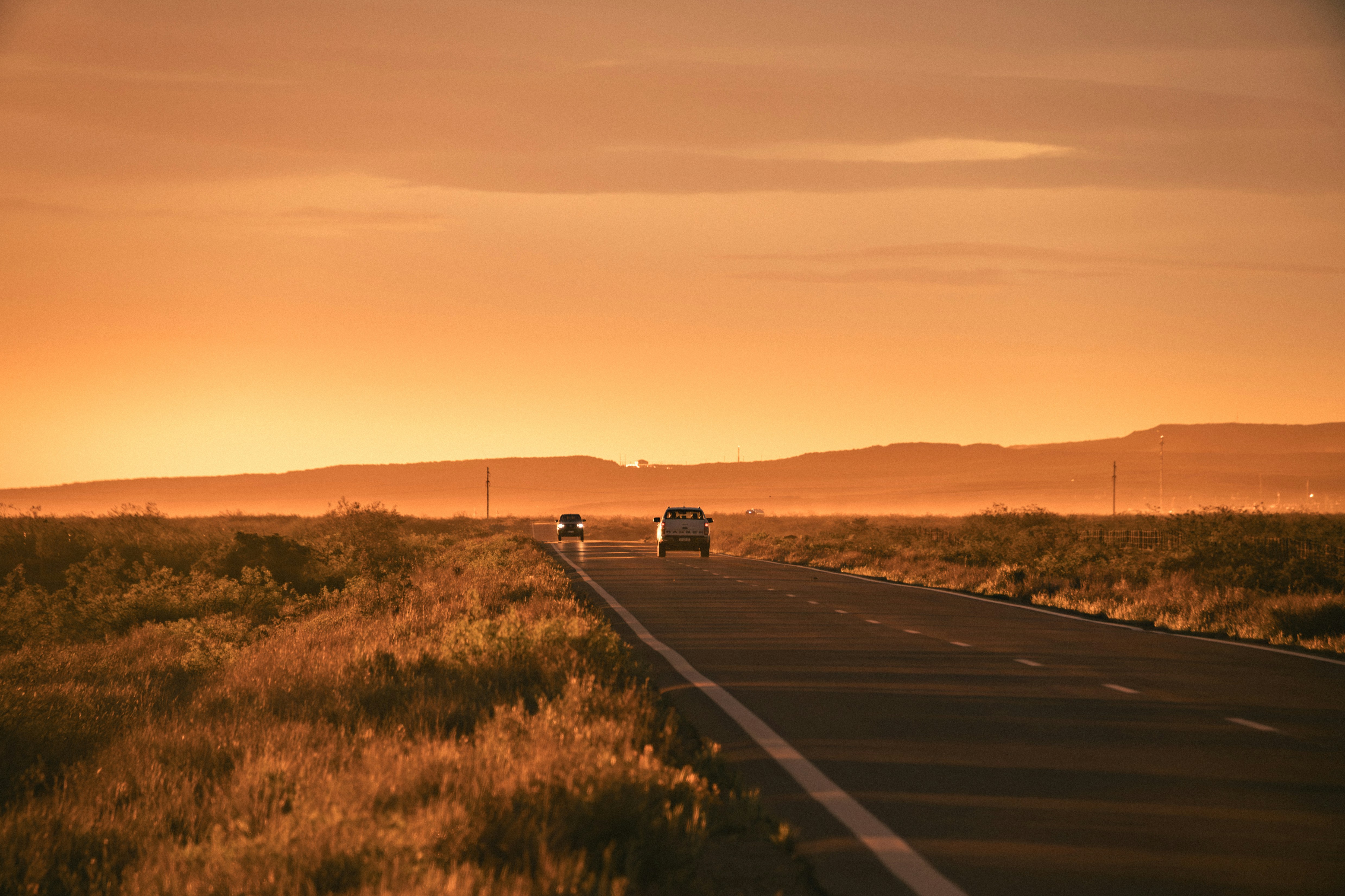Golden Hour Trek: Two Cars Move Along a Desert Highway Toward the Distant Horizon