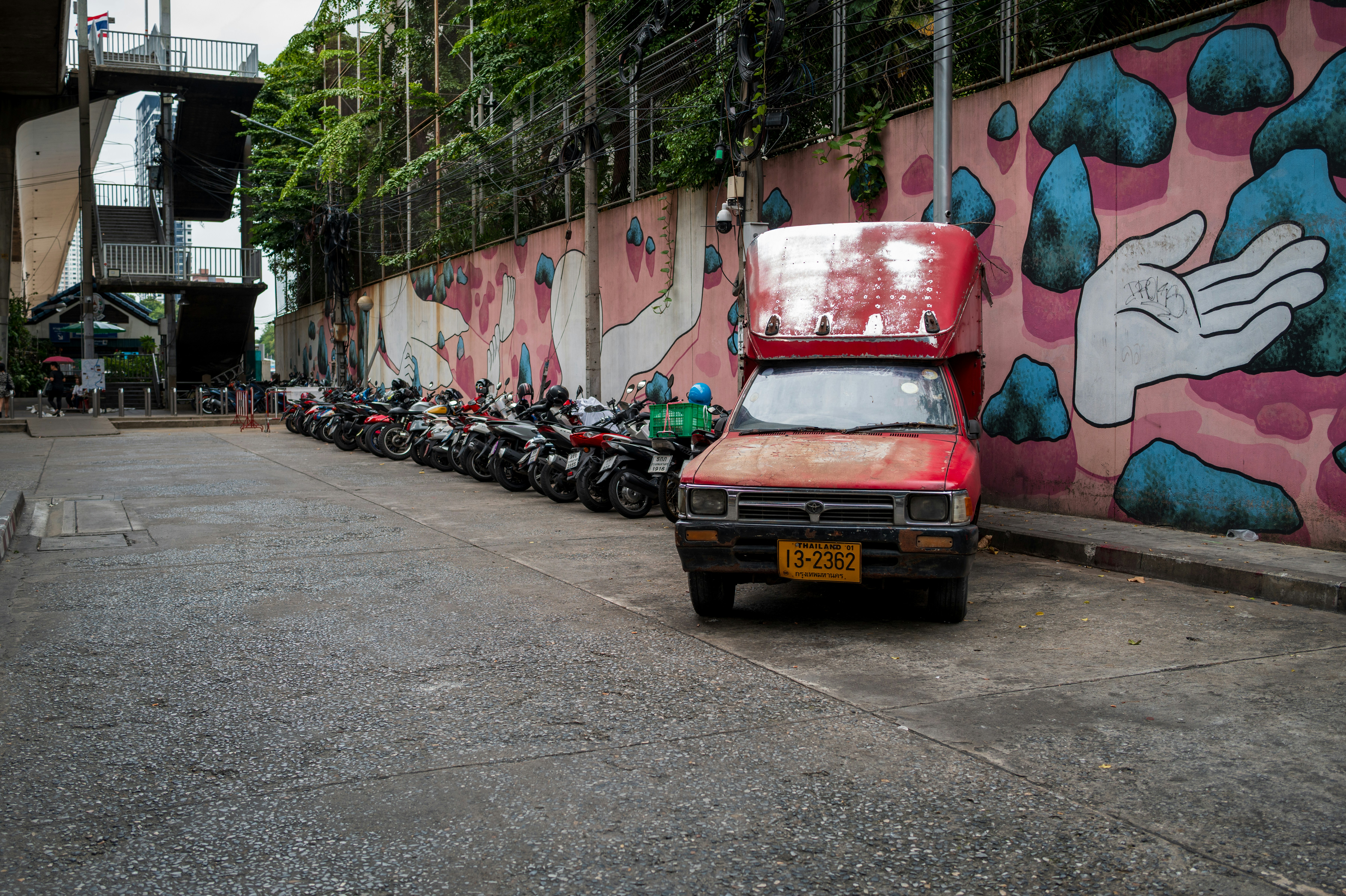 Red delivery van anchors a mural-lined alley beside a row of parked scooters