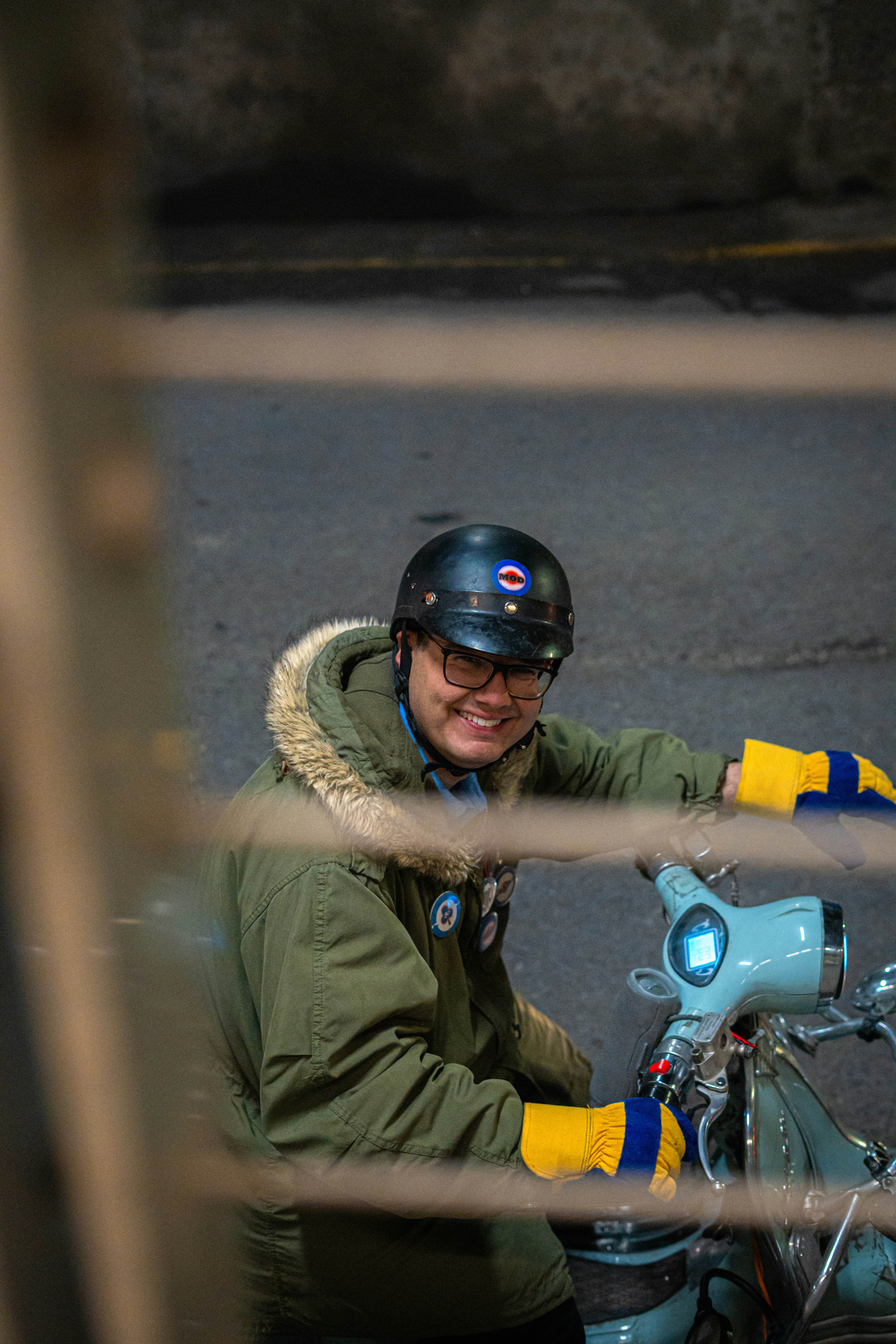 Smiling rider on a mint-teal vintage scooter framed by urban rails