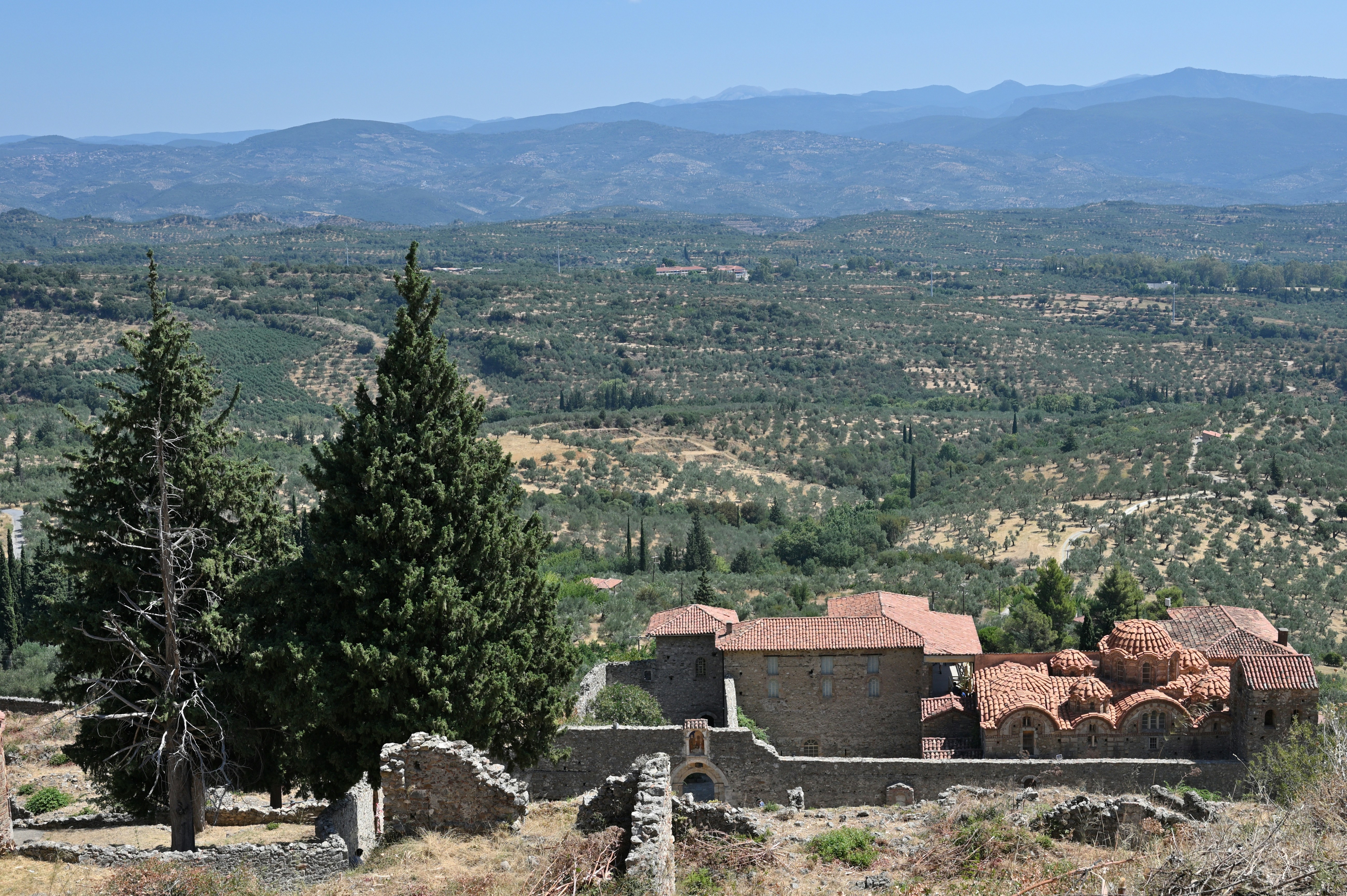 Red-Roofed Ruins Over Olive Terraces Beneath a Looming Mountain Range