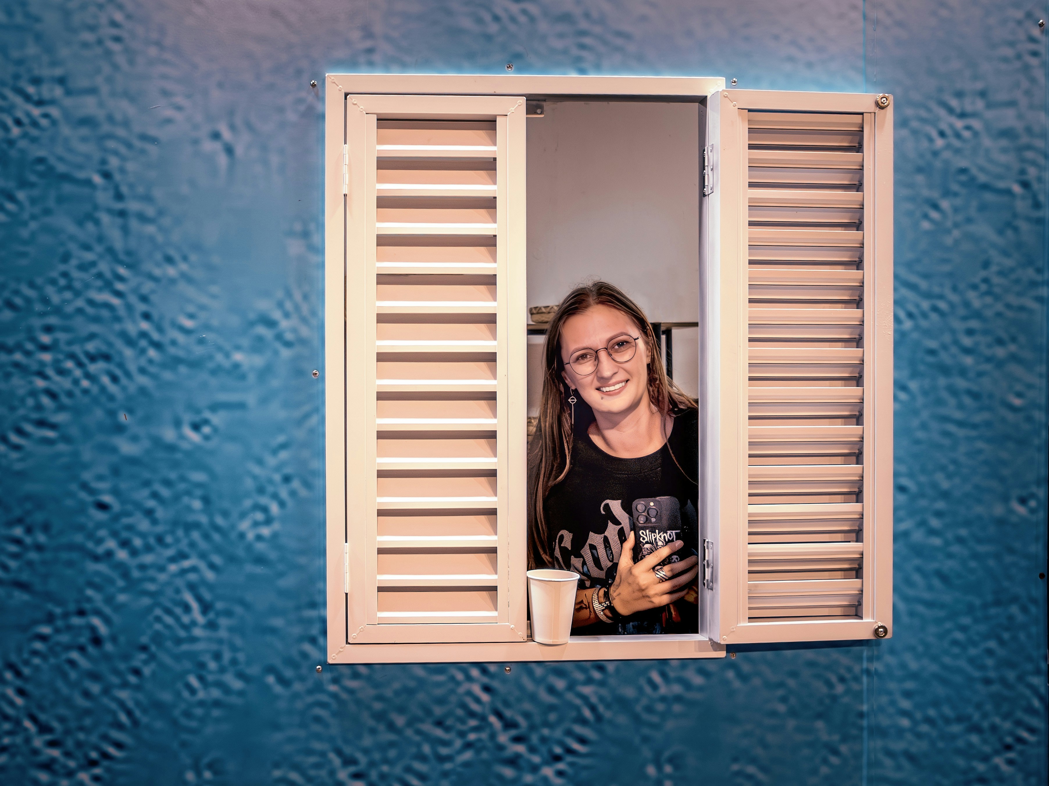 Young woman smiles from a window with shutters
