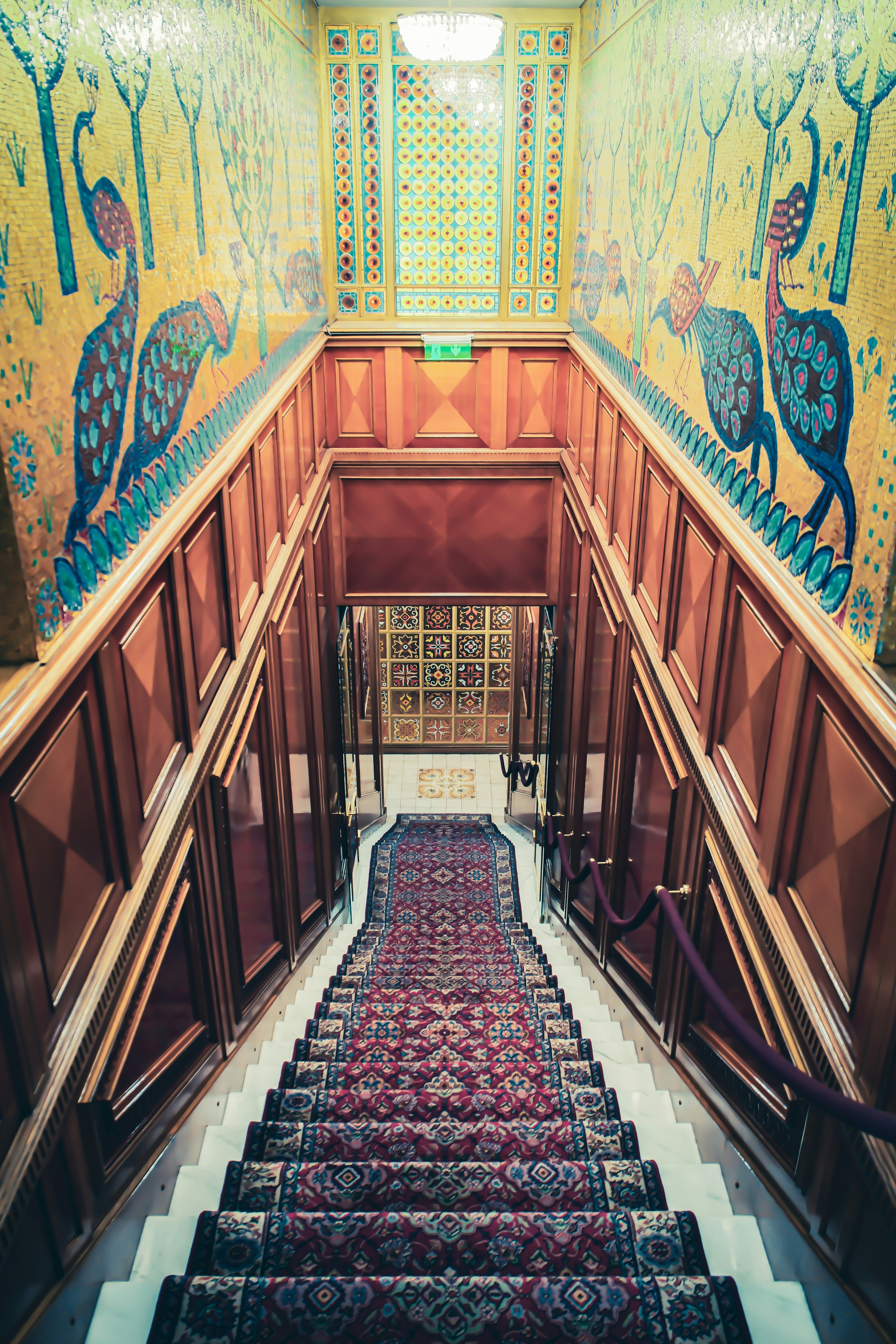Descend Through Peacock Murals: A Staircase Framed by Warm Wood and Persian Carpet
