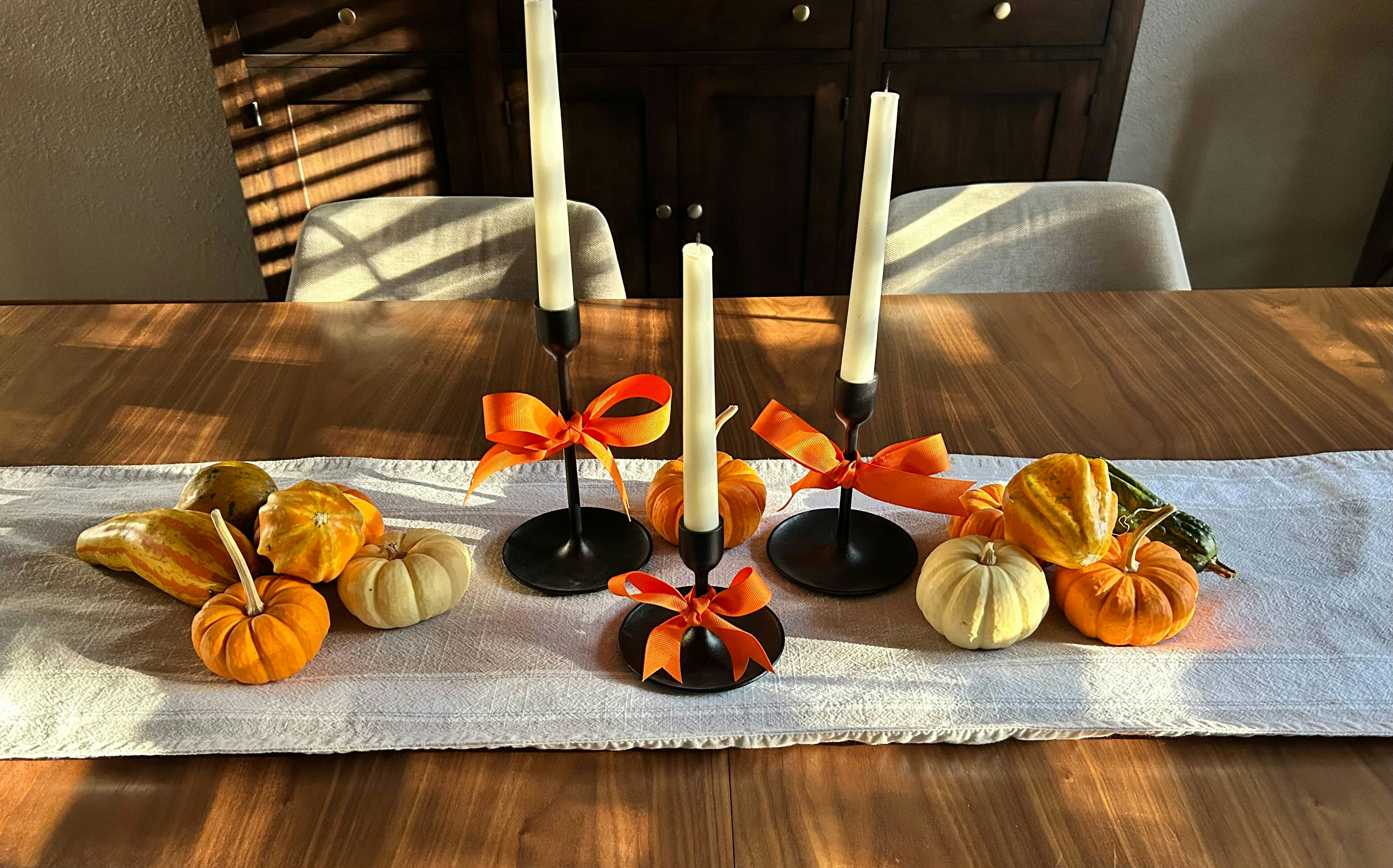 Candlesticks with pumpkins and gourds on a table runner.