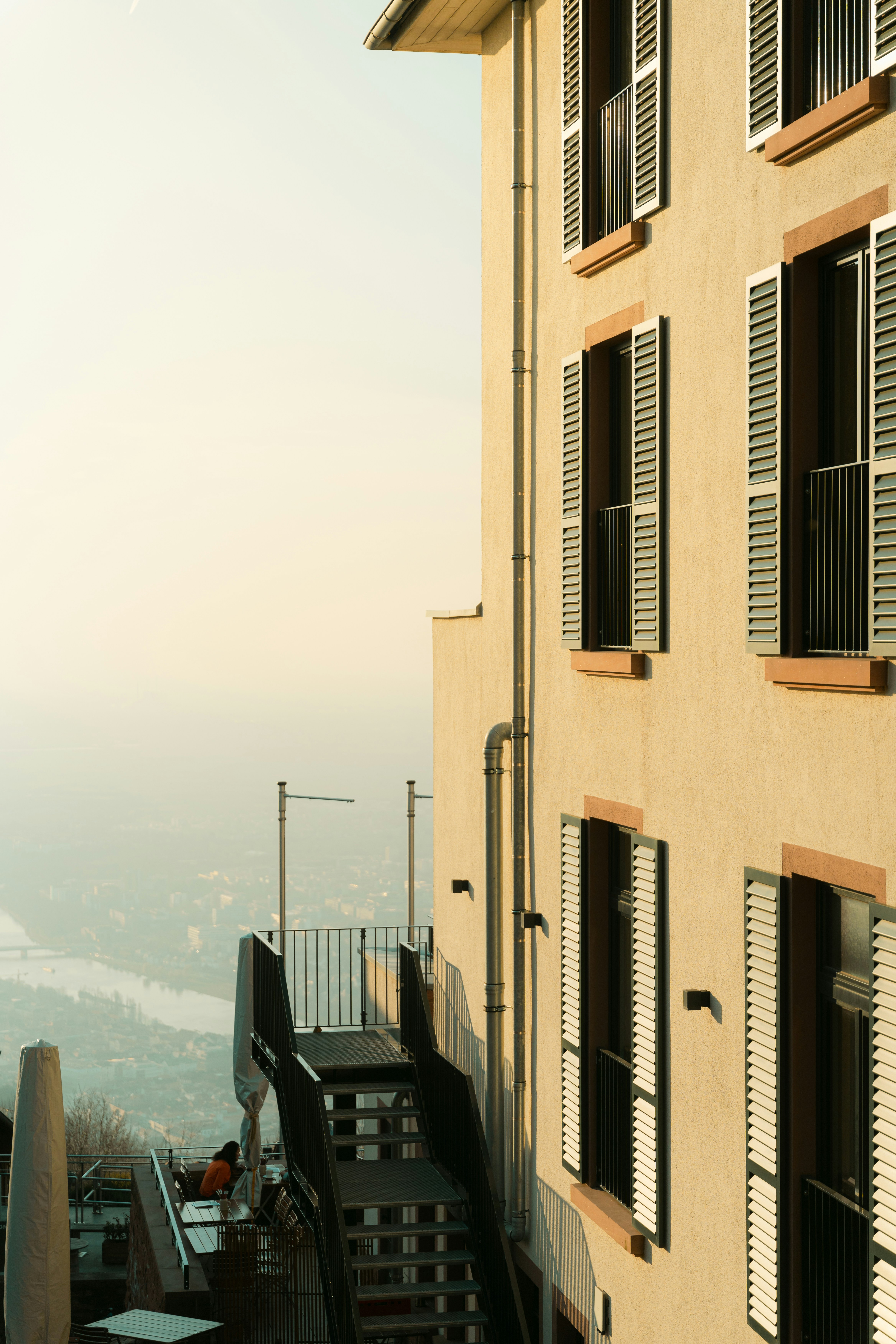 Sunlit Facade Vista: Staircase and Shuttered Windows with a Distant Riverside Horizon