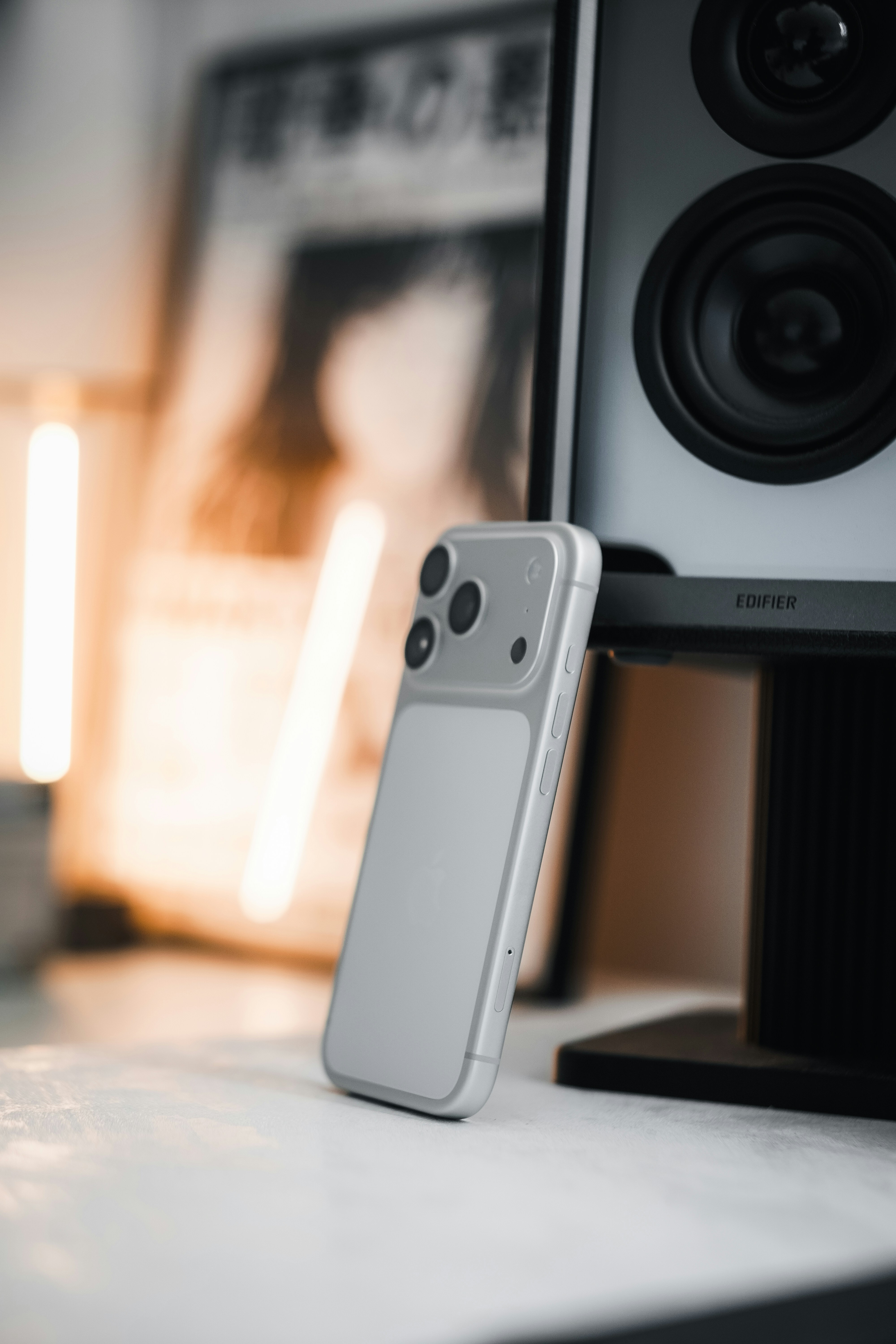 Neon Quiet: A Silver Smartphone Leaning by a Speaker in Soft Indoor Glow