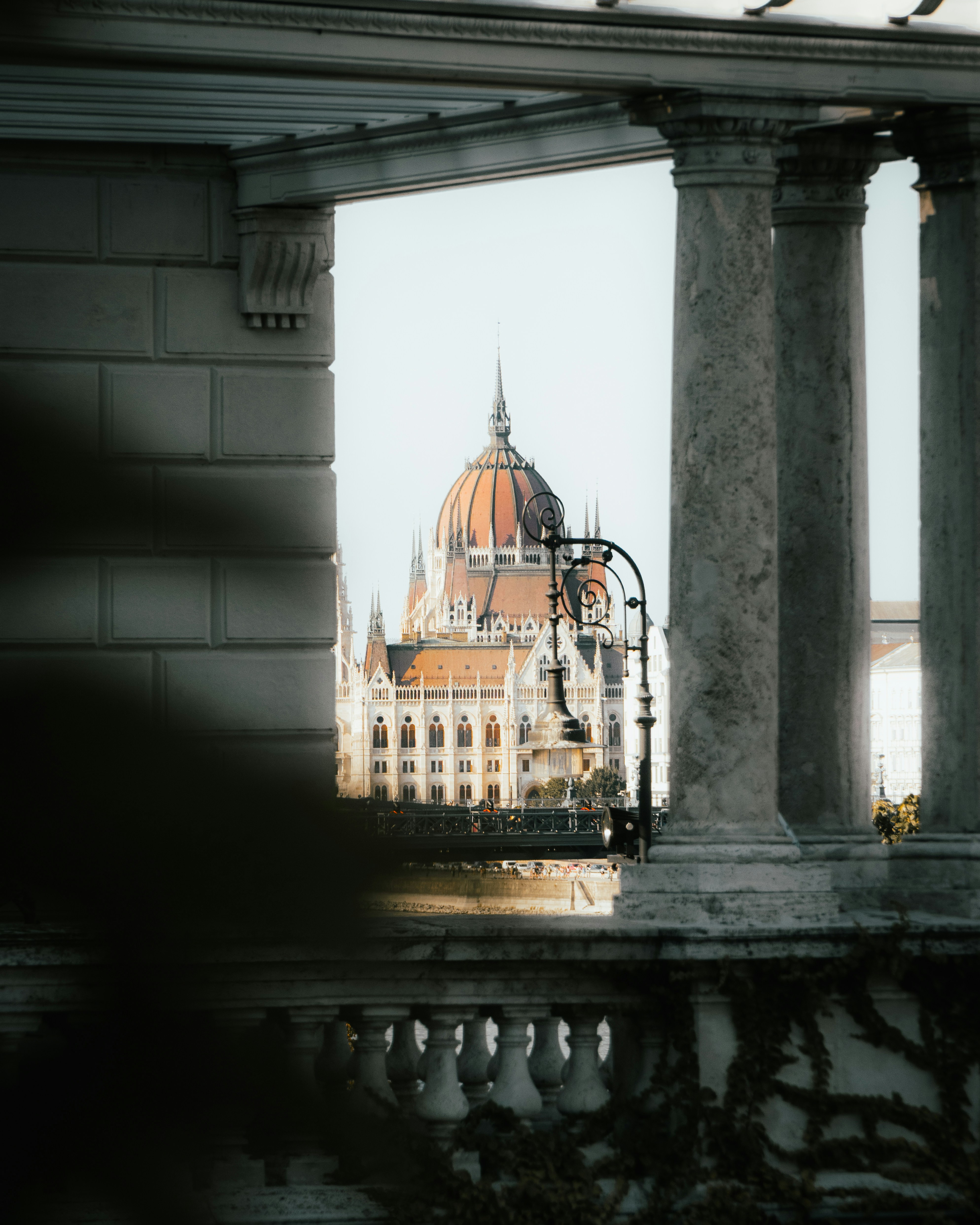 Copper Crown Through Stone: Budapest Parliament Framed by Timeworn Colonnades