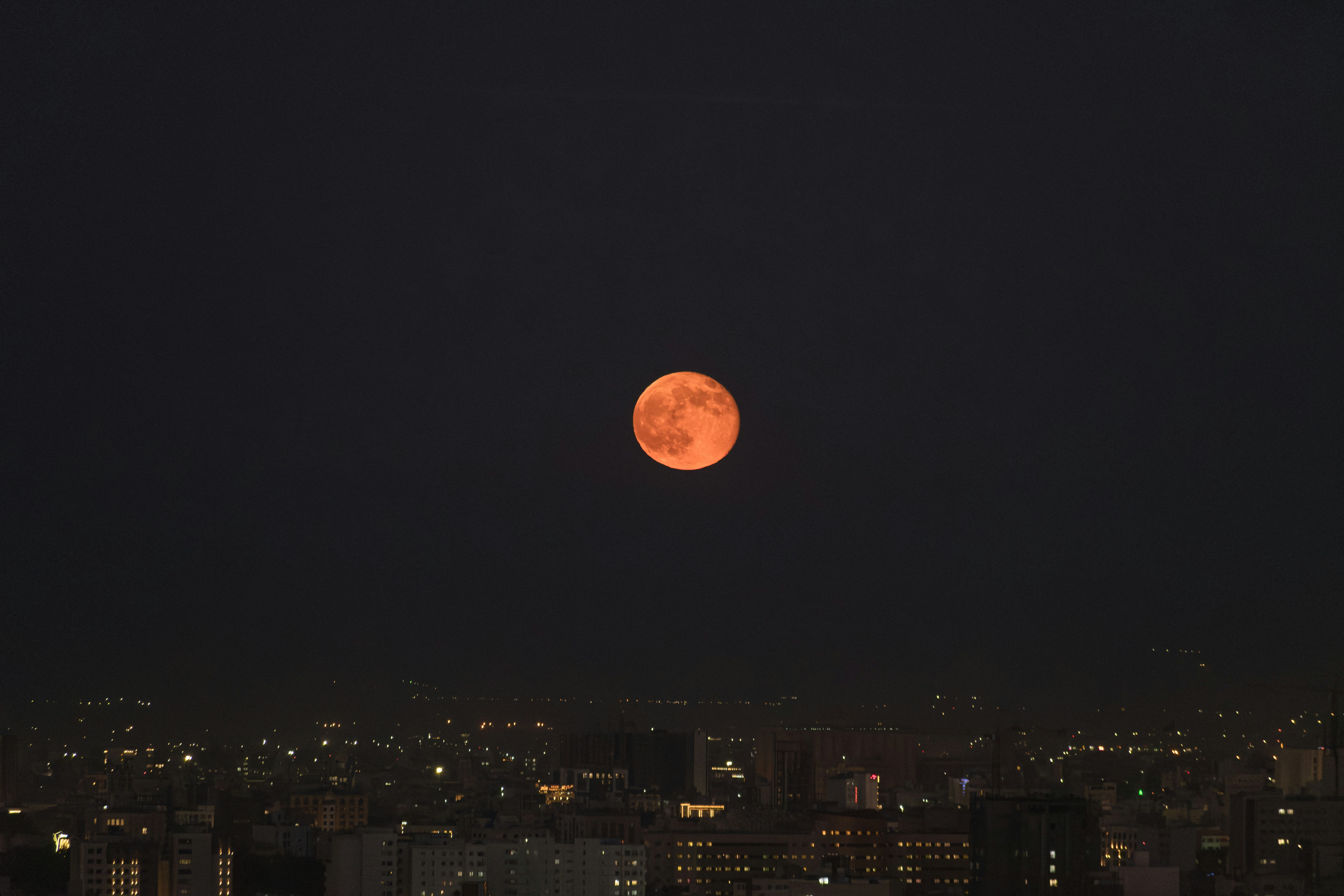 A large orange moon hangs over a city at night. photo – Free Space ...