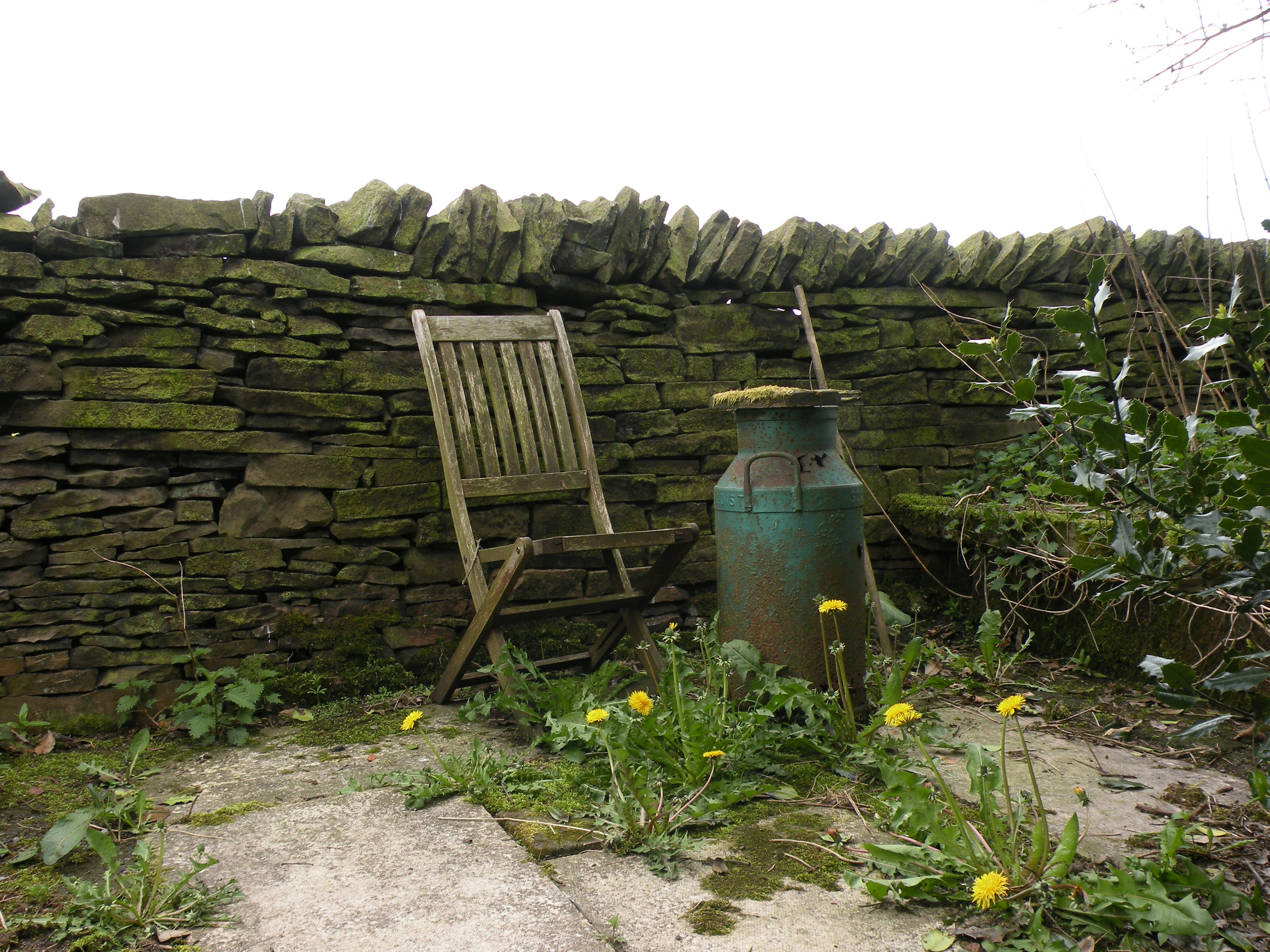 Wooden chair and milk churn by stone wall